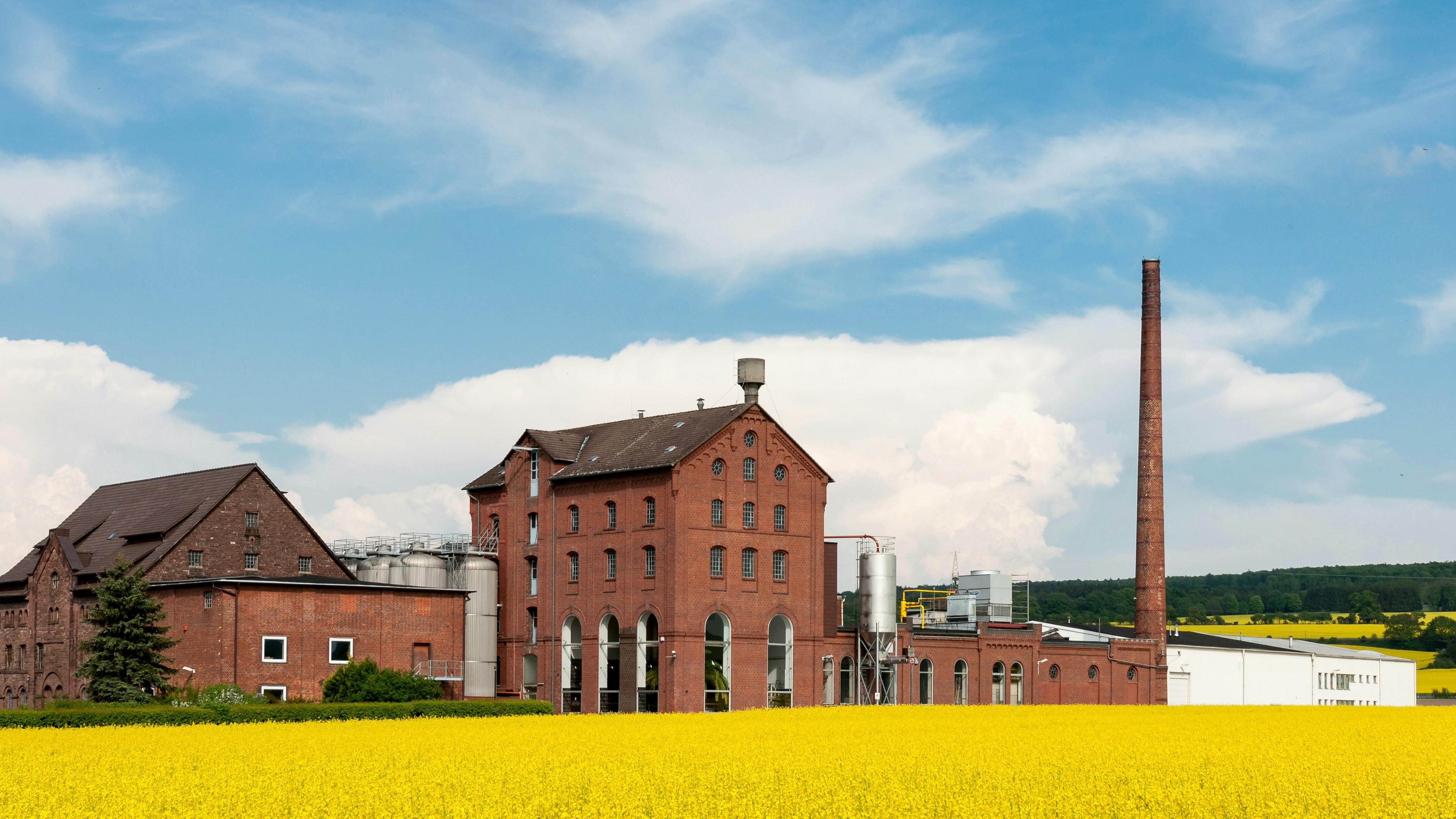 Brick factory building with tall chimney in yellow field.