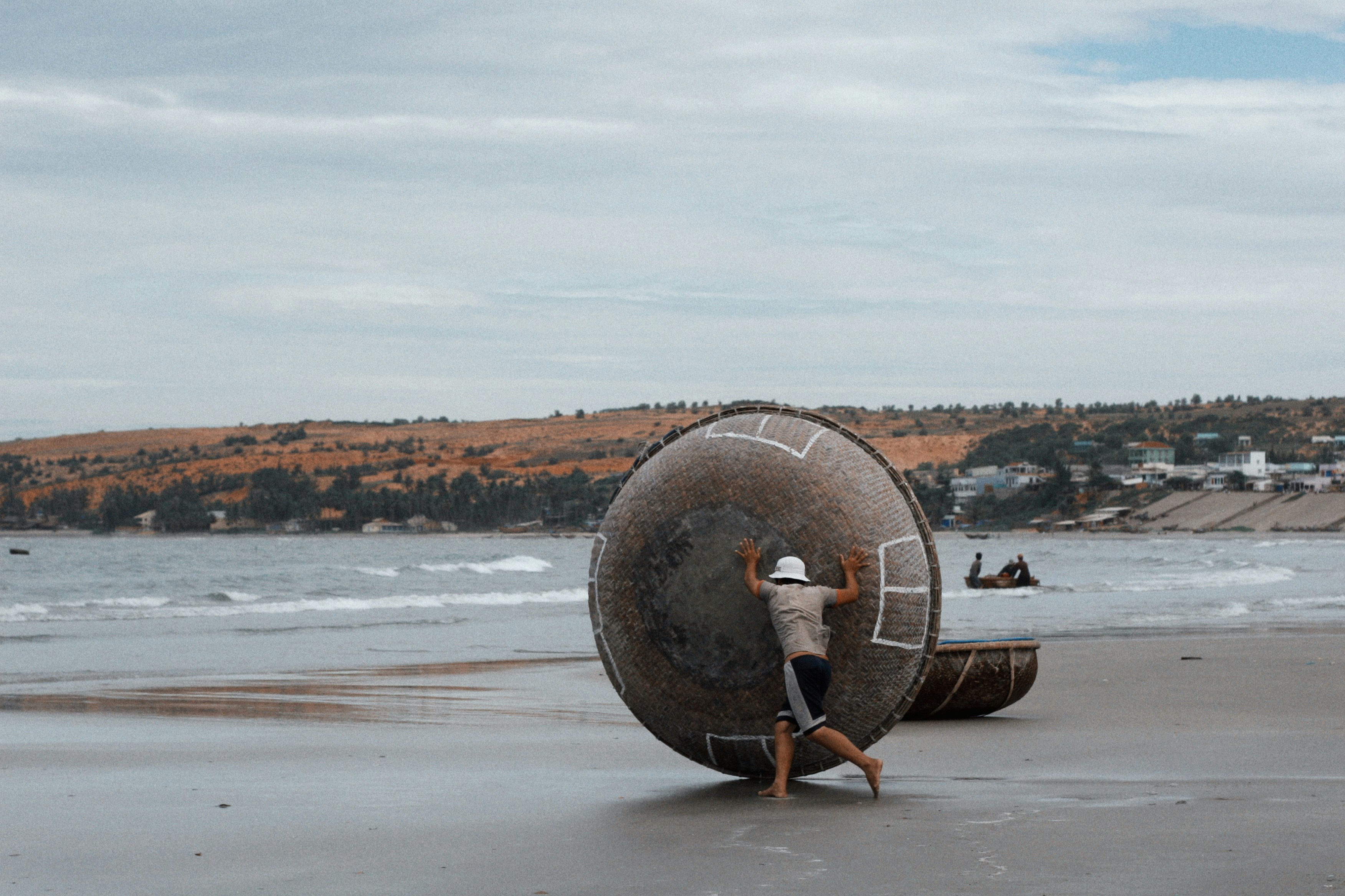Man pushing large woven basket on a sandy beach.