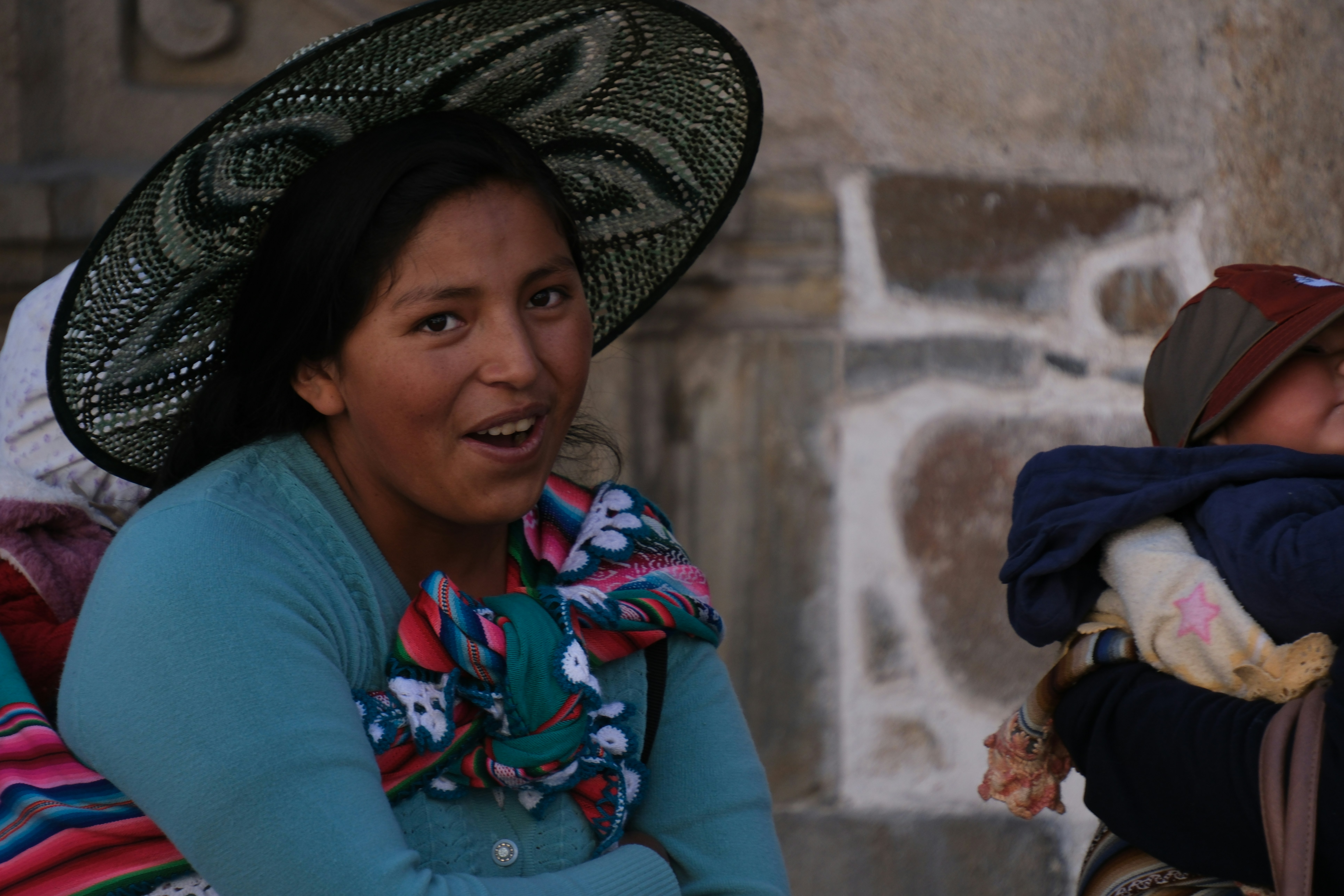 Woman in a wide-brimmed hat smiles while holding a baby.