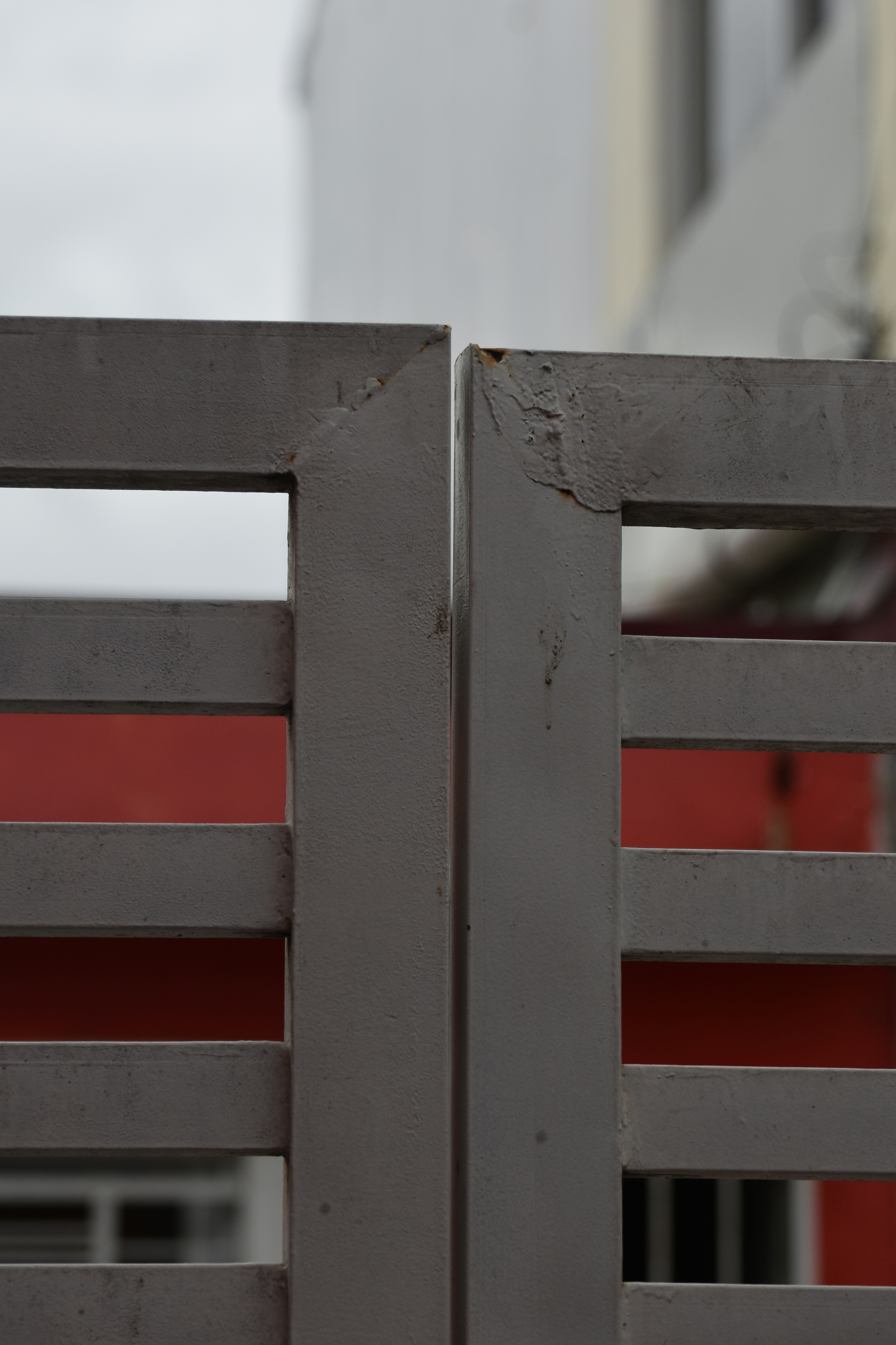 Close-up of a weathered metal gate with red background.