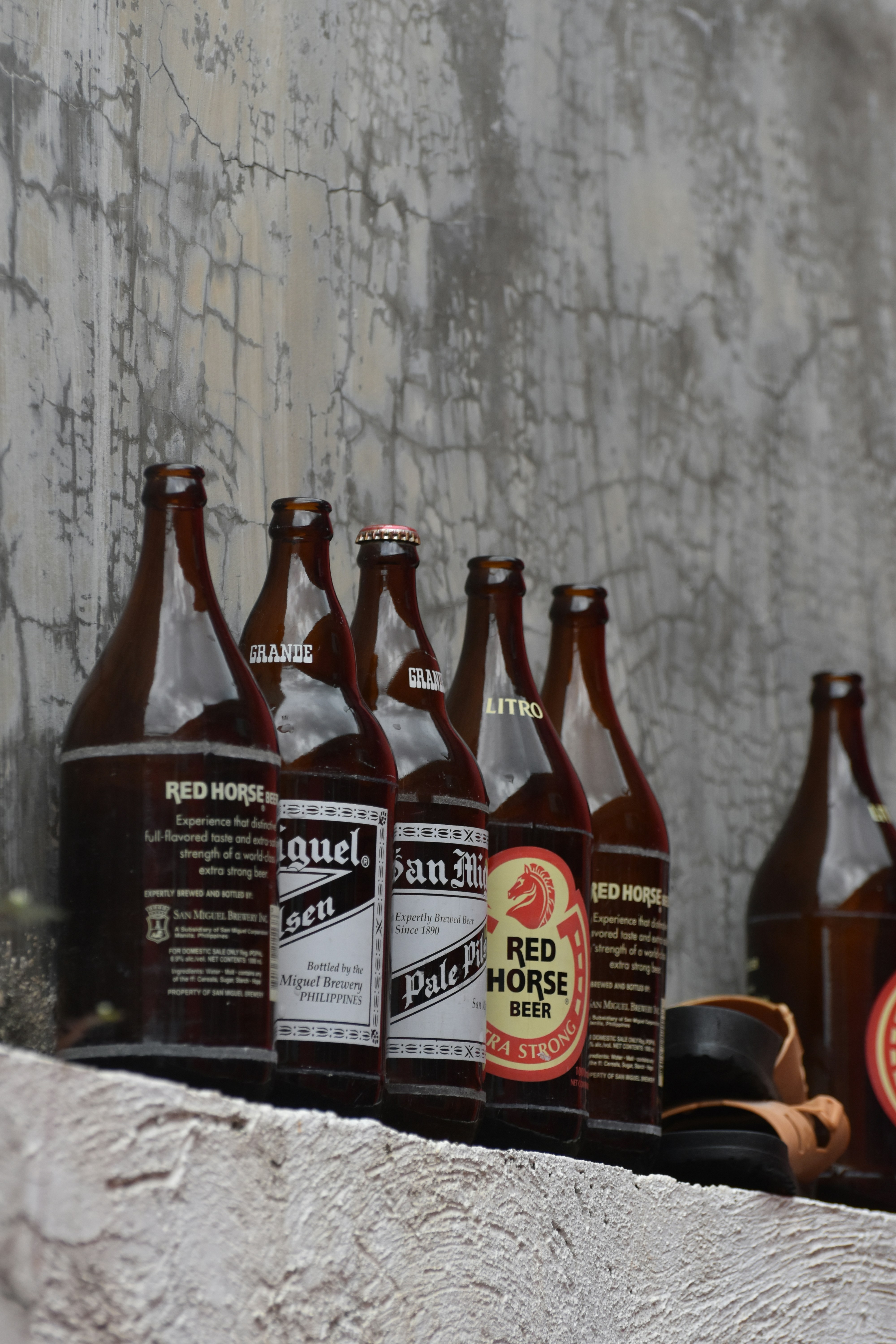 Collection of vintage beer bottles lined against a textured wall, showcasing local brews and their distinct labels.