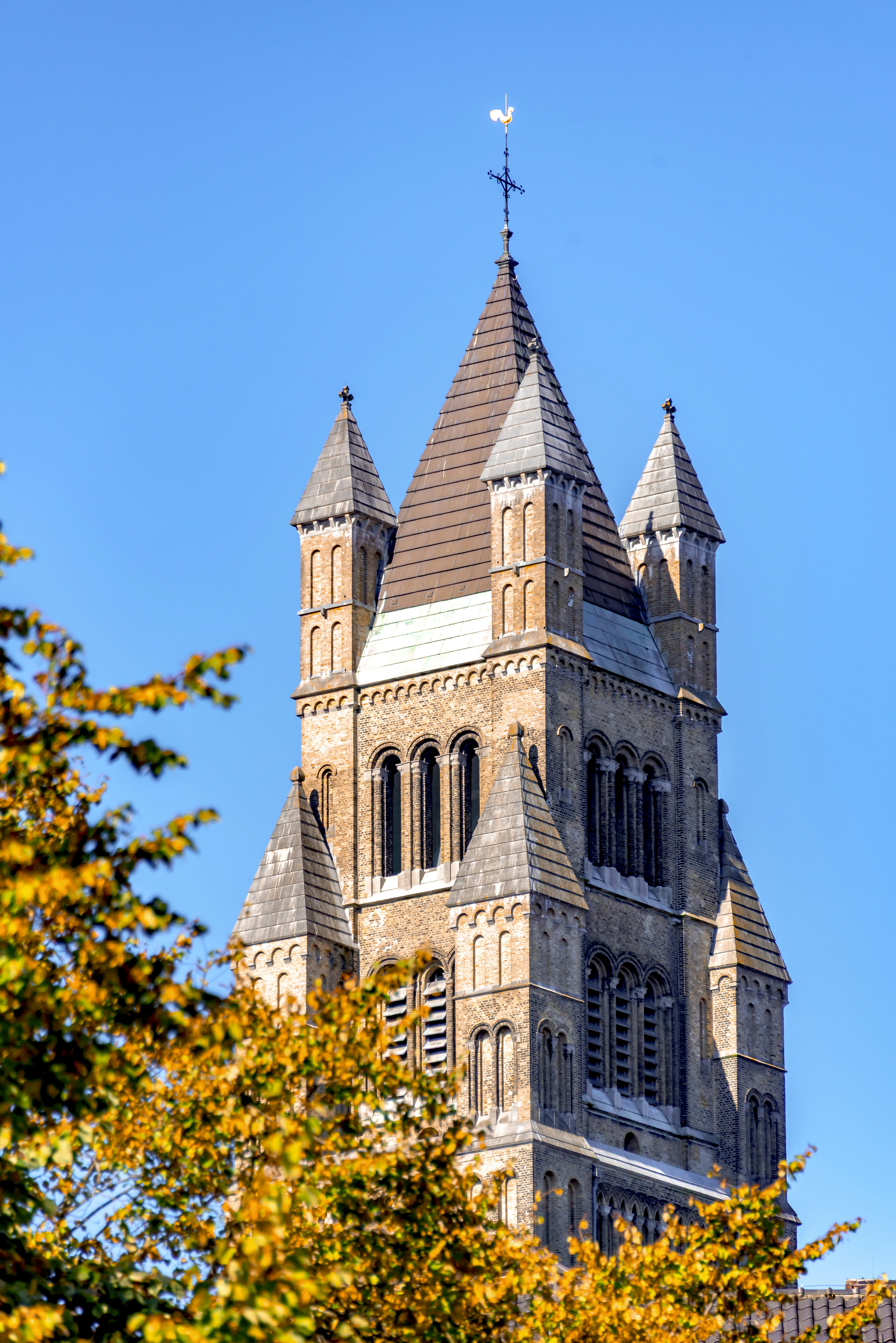 Tall church tower with autumn trees against blue sky.