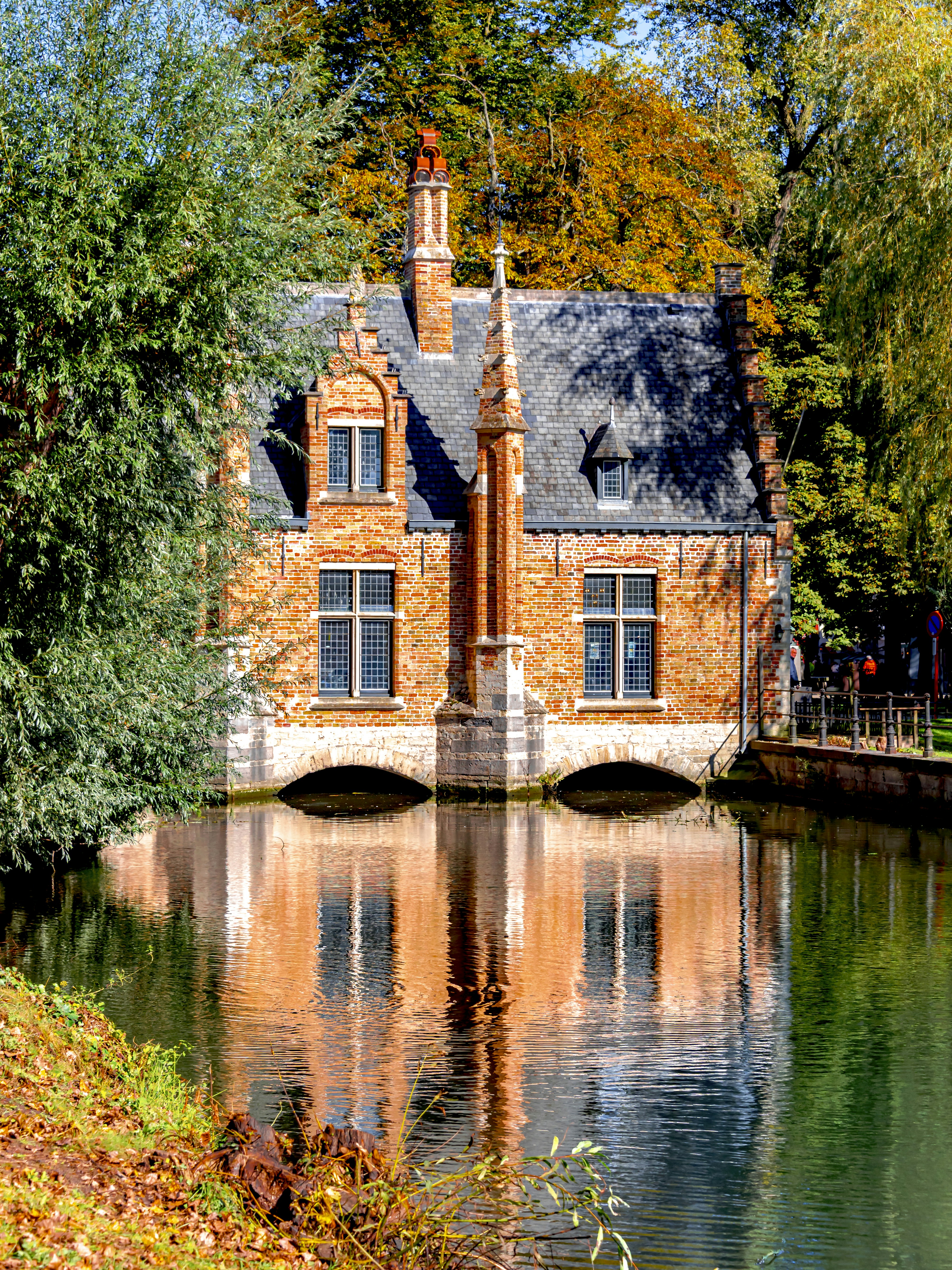Brick building reflected in canal surrounded by trees