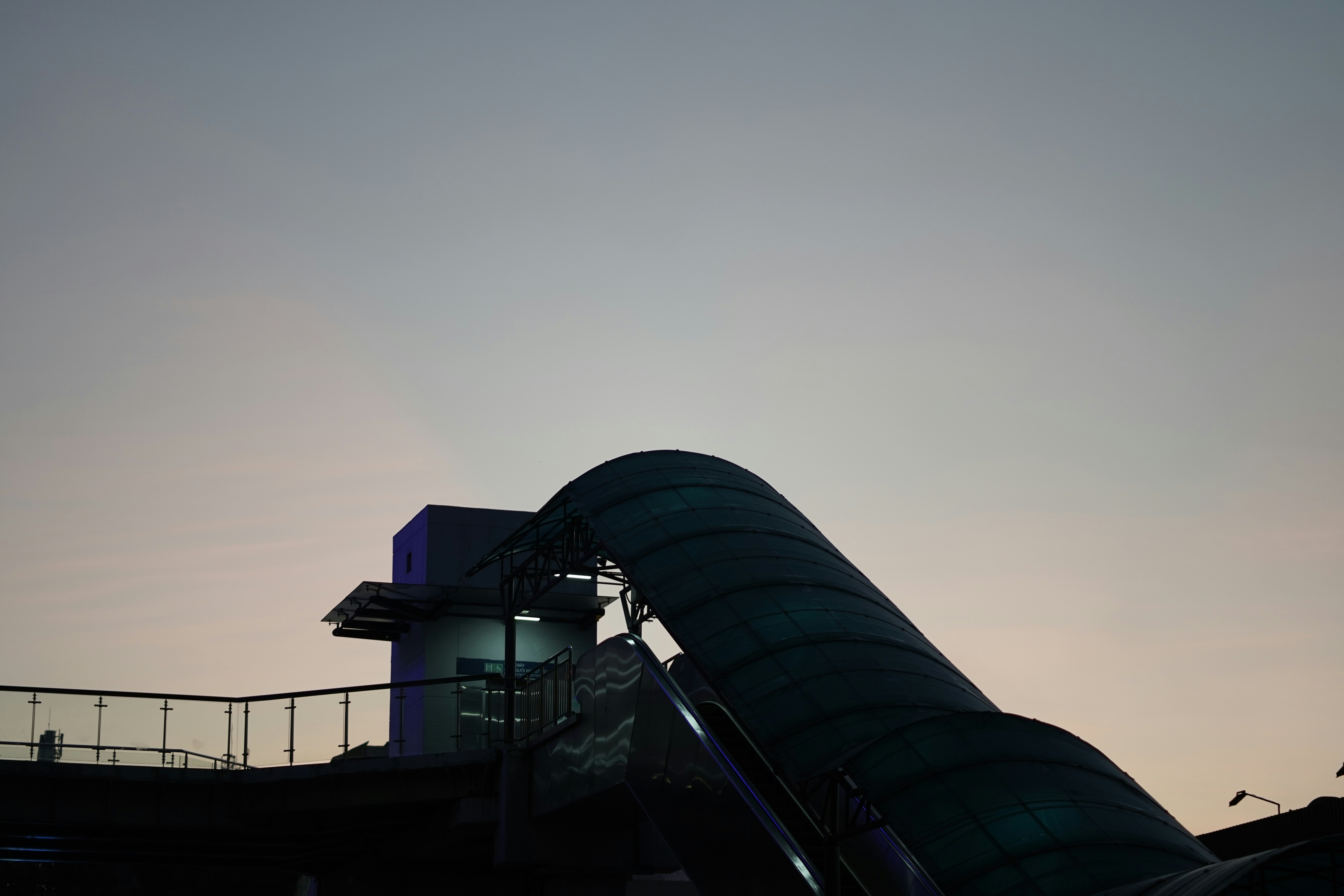 A modern architectural structure with a sweeping curve, silhouetted against a pastel twilight sky.