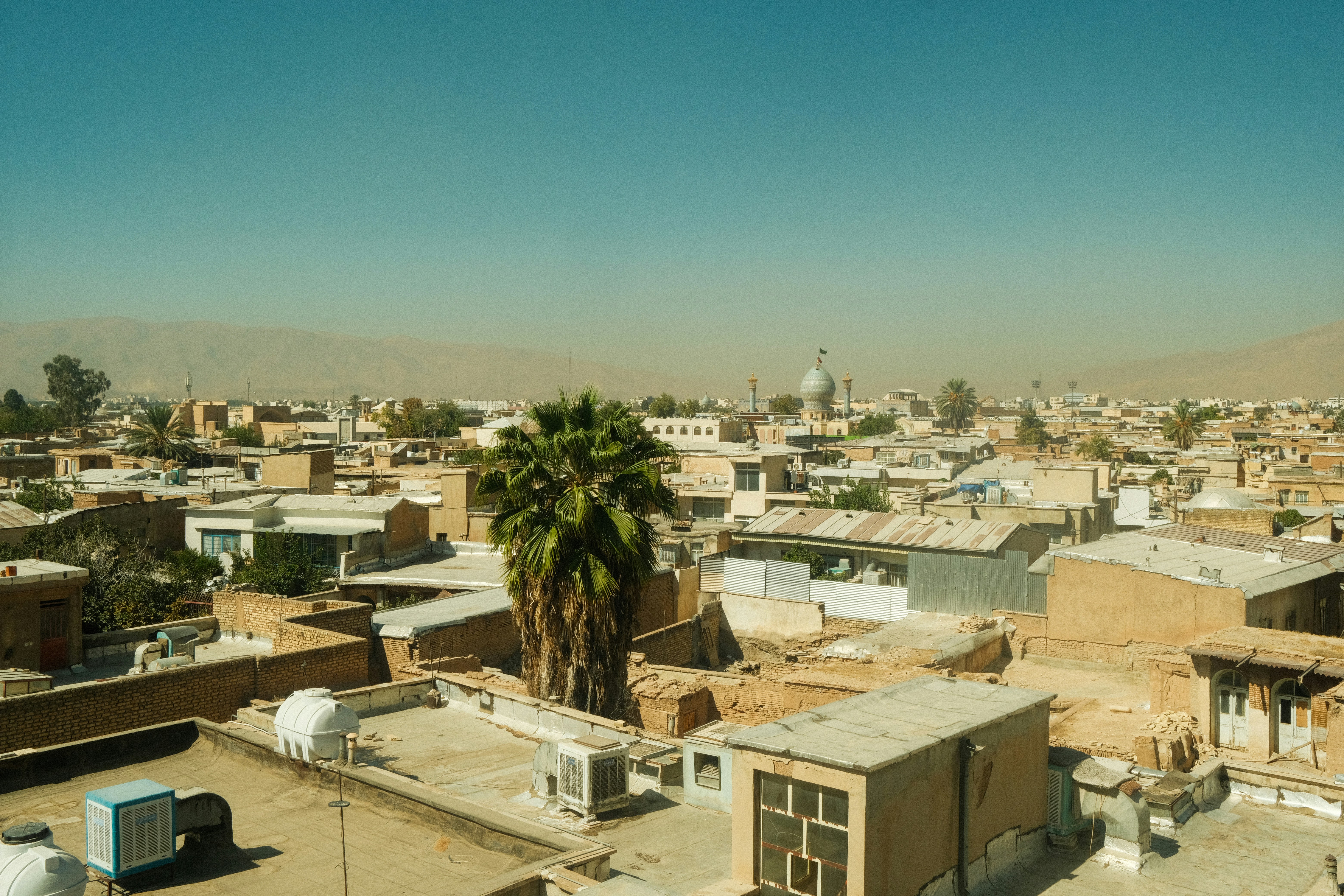 Overhead view of a dusty middle eastern city with palm trees.