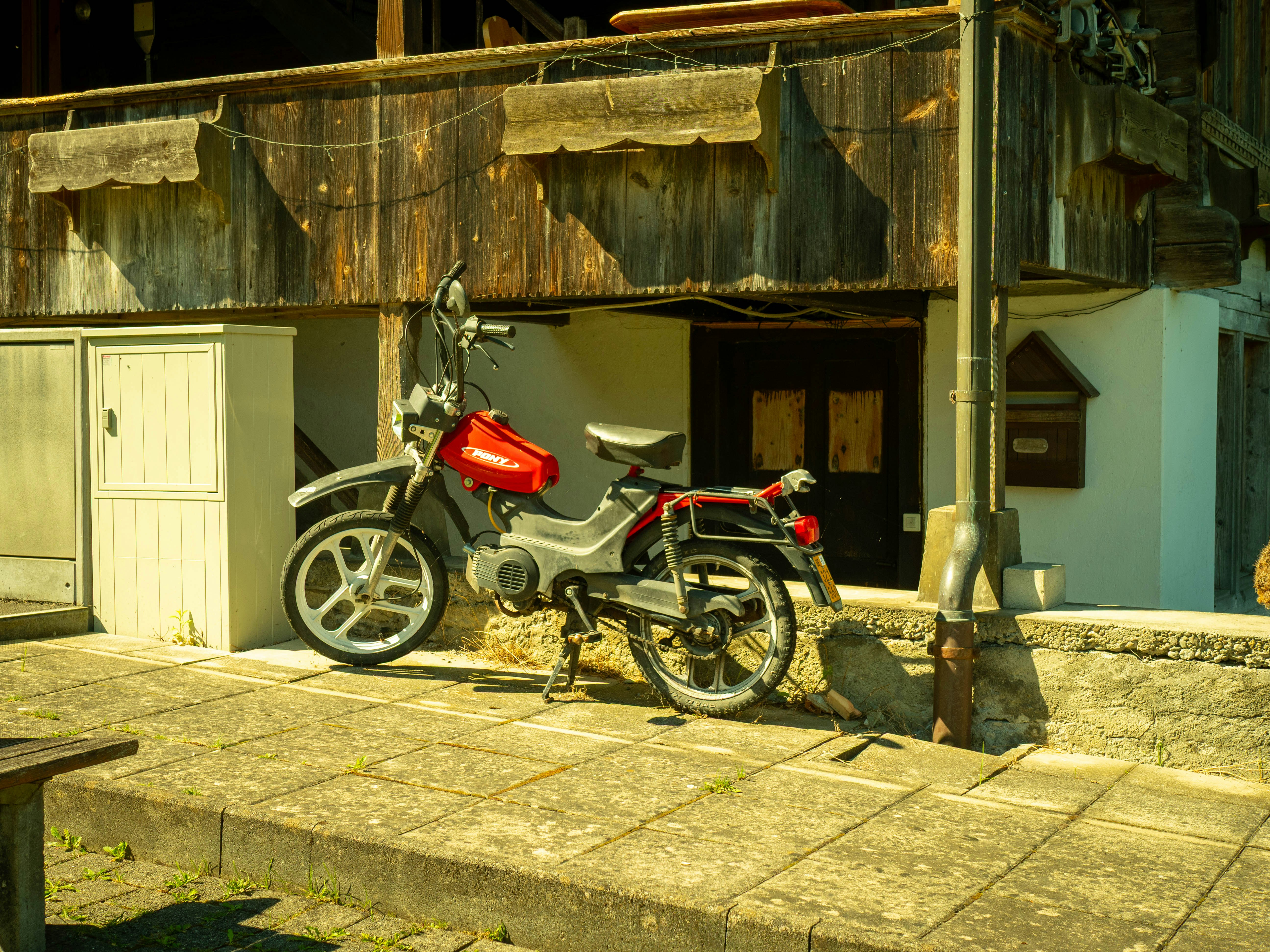Pony-Moto | Red scooter parked outside a wooden building