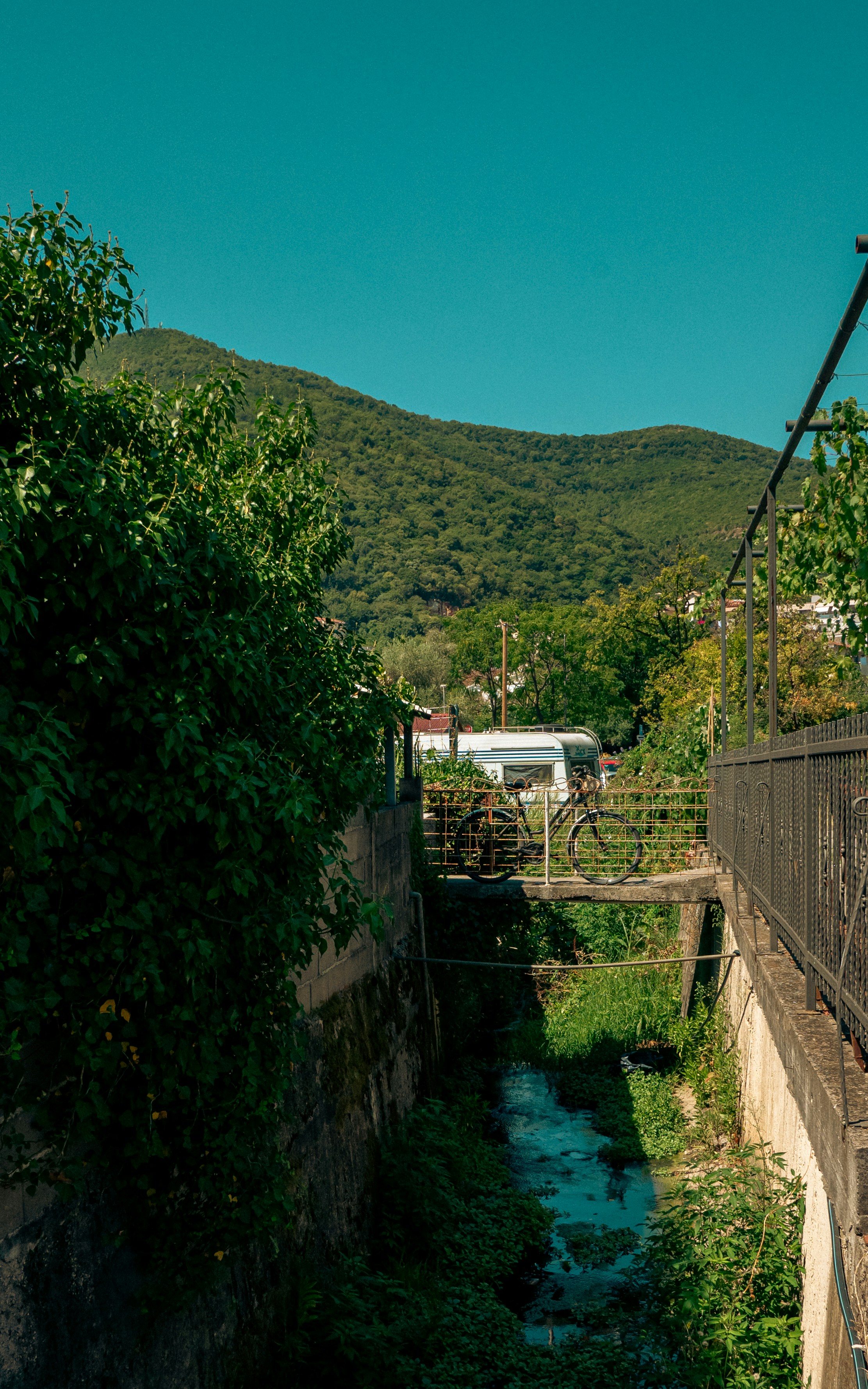 mount | A stream flows under a bridge with a bicycle.