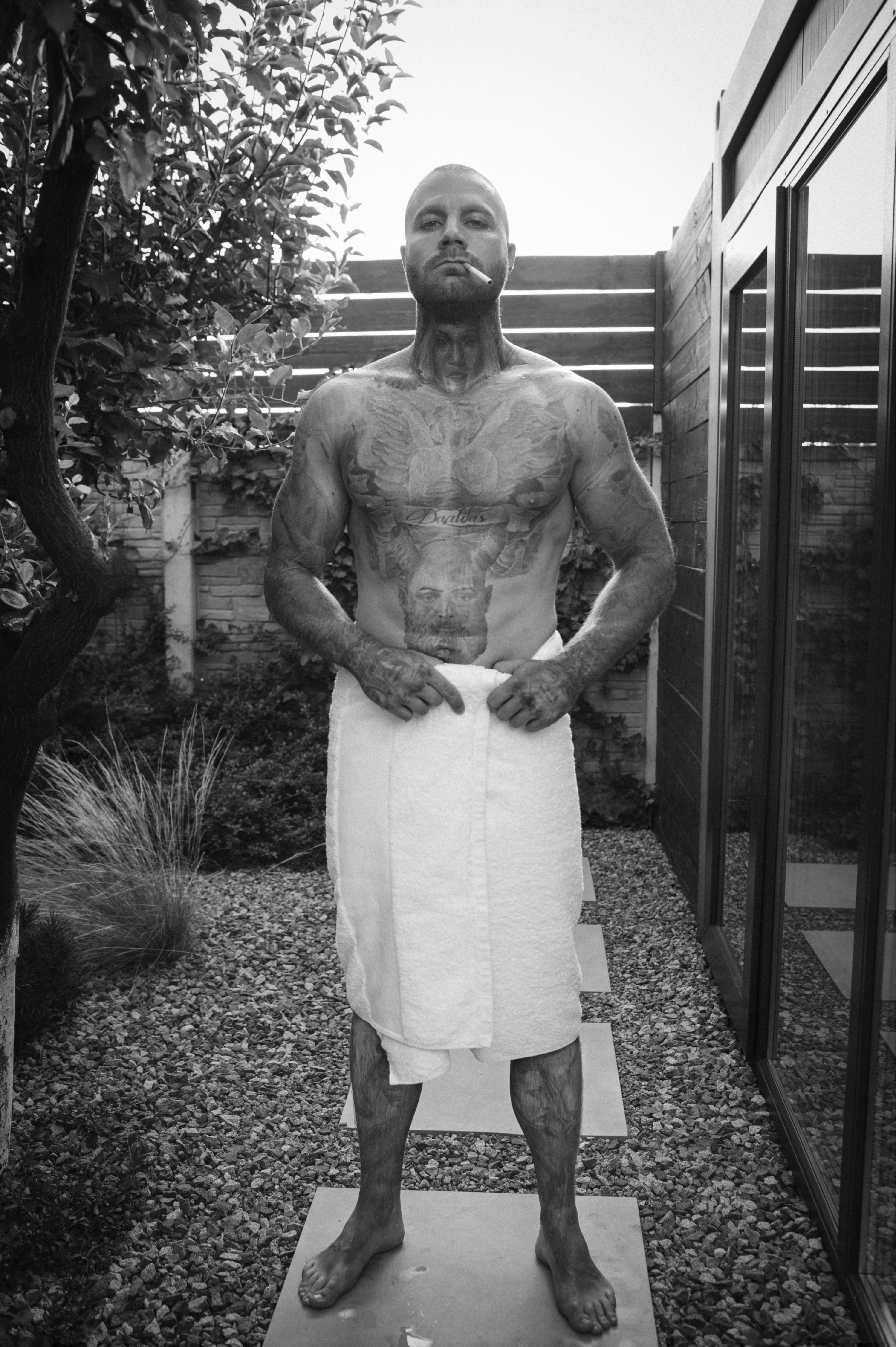 Stance in Steel-and-Glass: A Tattooed Physique Anchored in a Quiet Courtyard