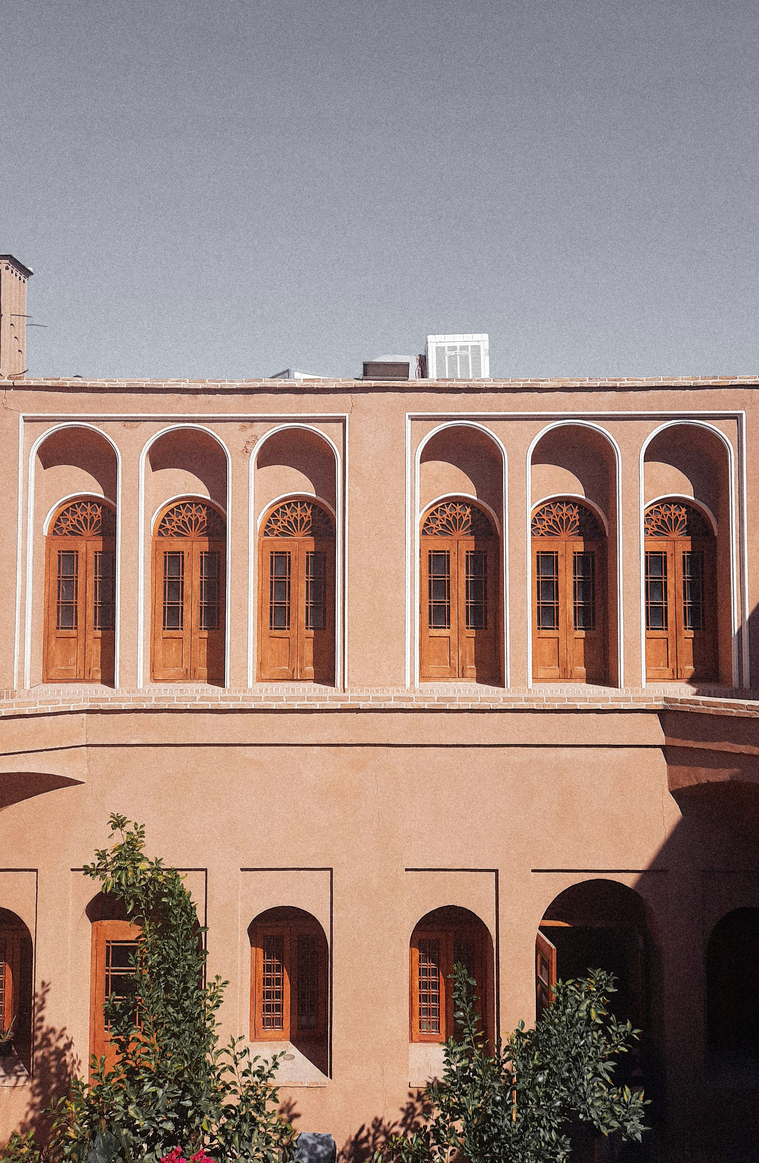 Elegant building facade featuring multiple arched windows and intricate wooden detailing, surrounded by lush greenery.
