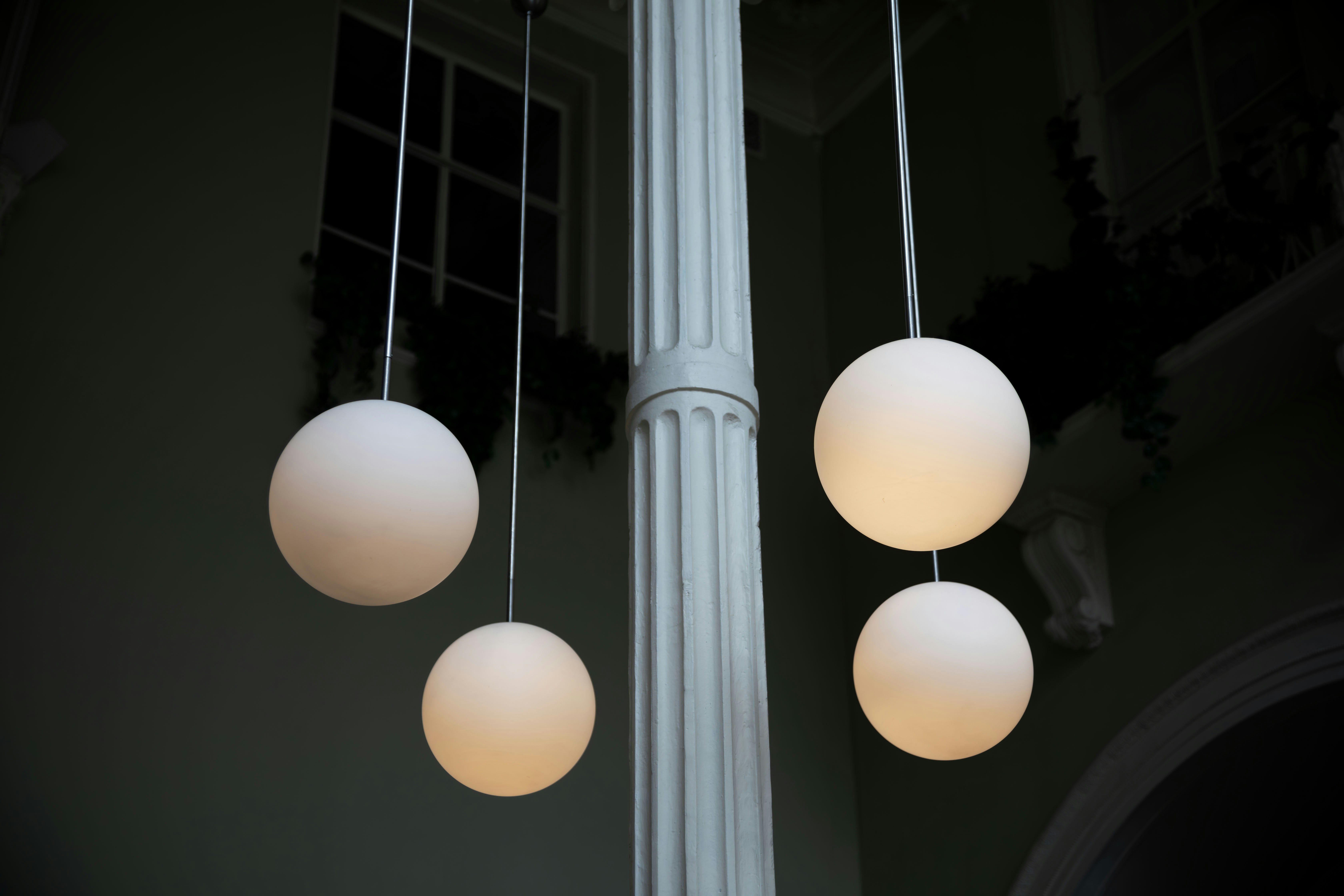 Four spherical pendant lights hanging from a column in a softly lit interior space.