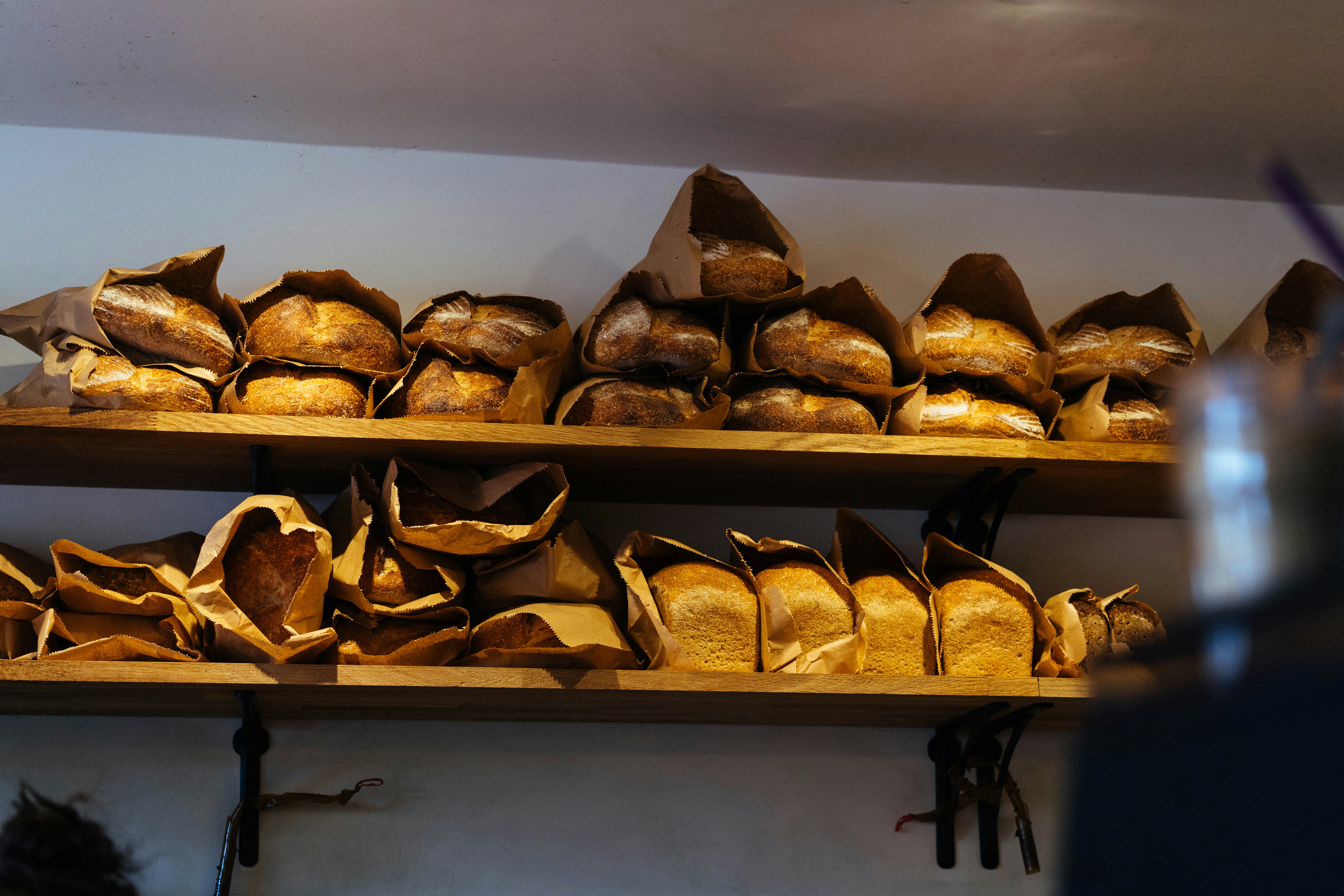 Neatly arranged artisan bread loaves in paper bags on wooden shelves, showcasing the craftsmanship of a local bakery.