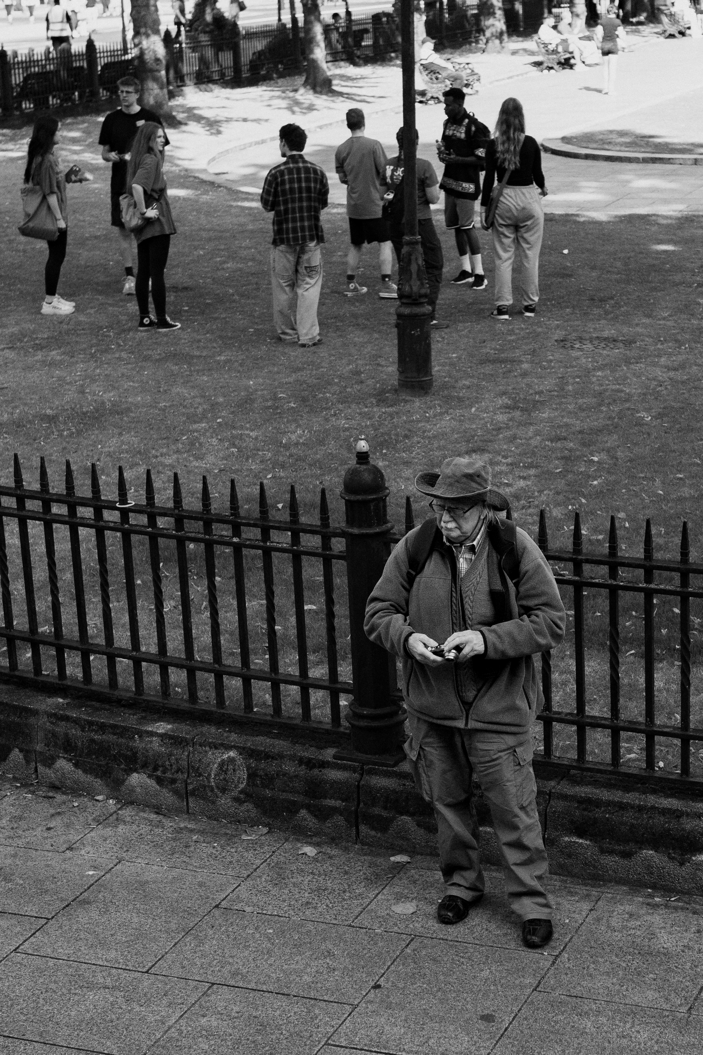 A Street Elder by the Iron Fence: Quiet Confidence in a Busy Square