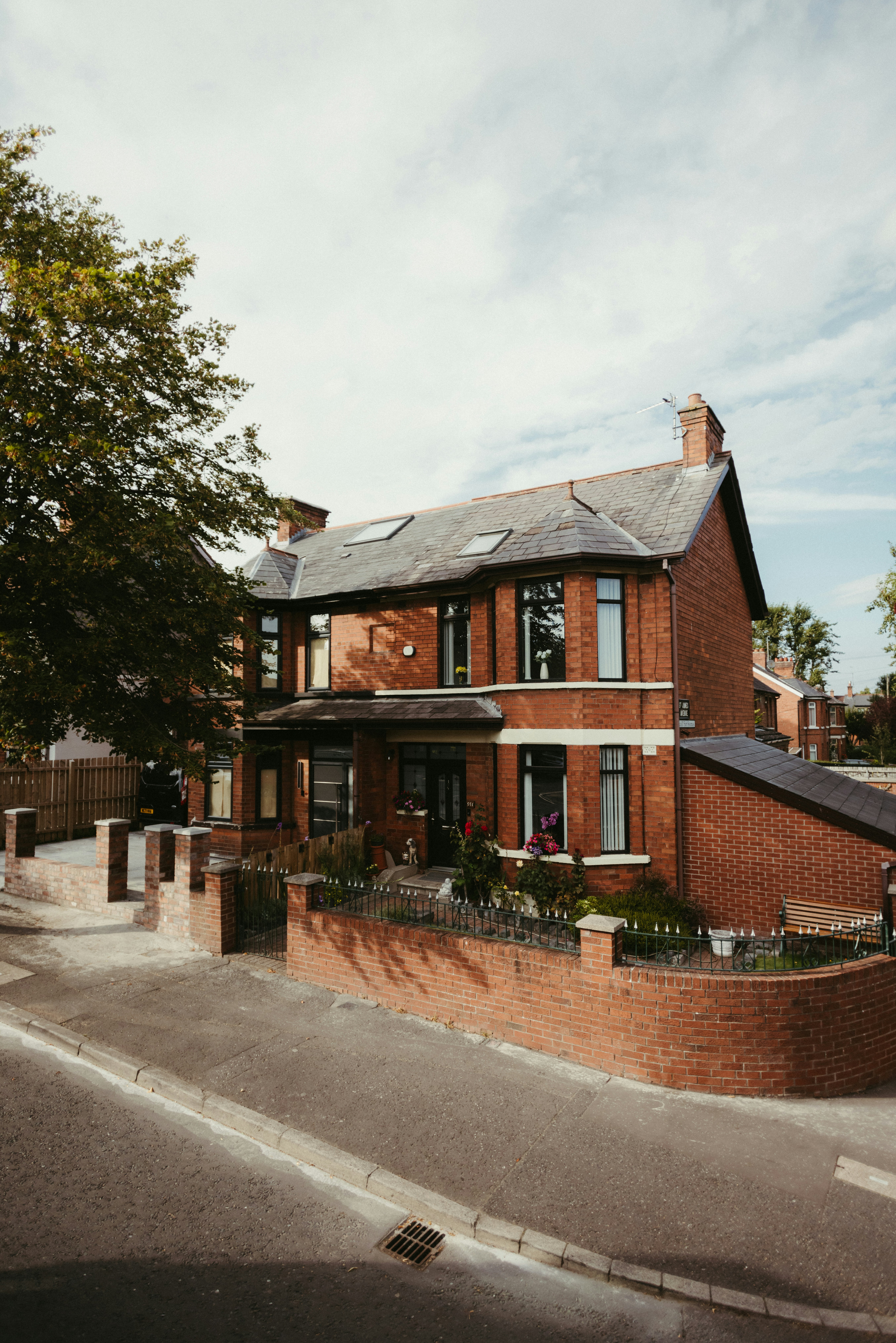 A beautifully designed brick house with a welcoming front garden, framed by lush trees and a clear blue sky.