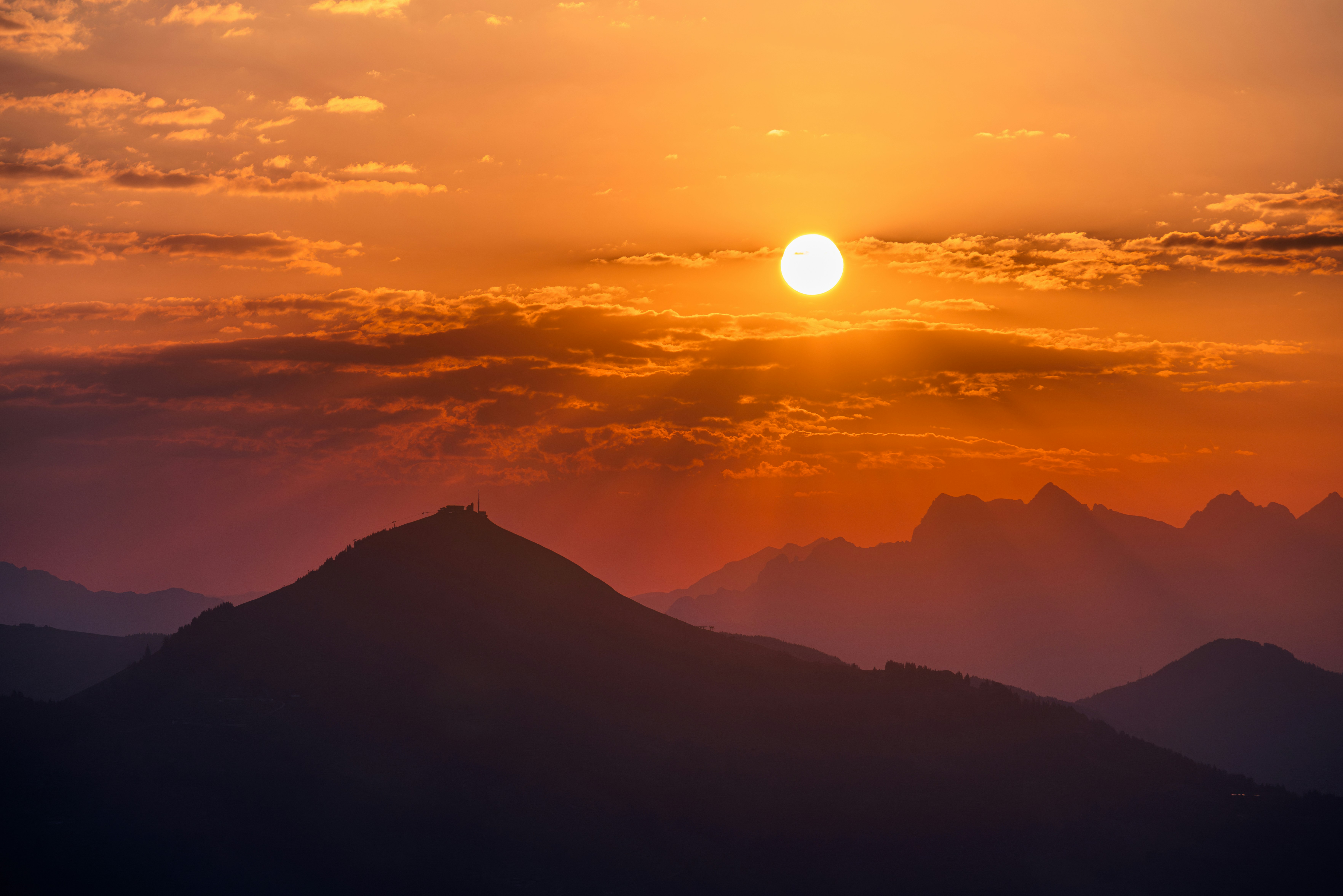Sun-Filled Sky Behind Majestic Peaks | Golden sun setting behind silhouetted mountain peaks.