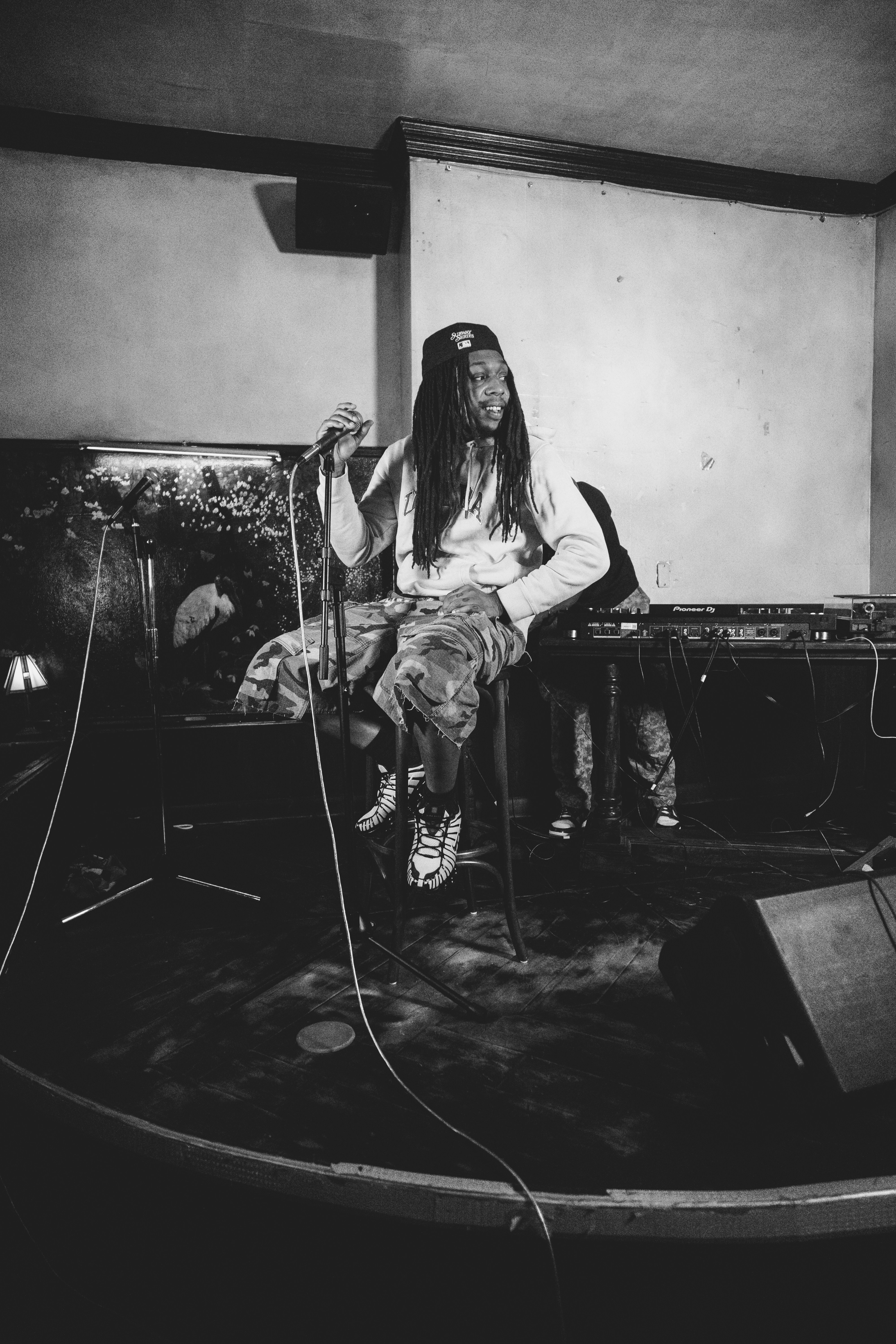 Man with dreadlocks sits on stage holding microphone.