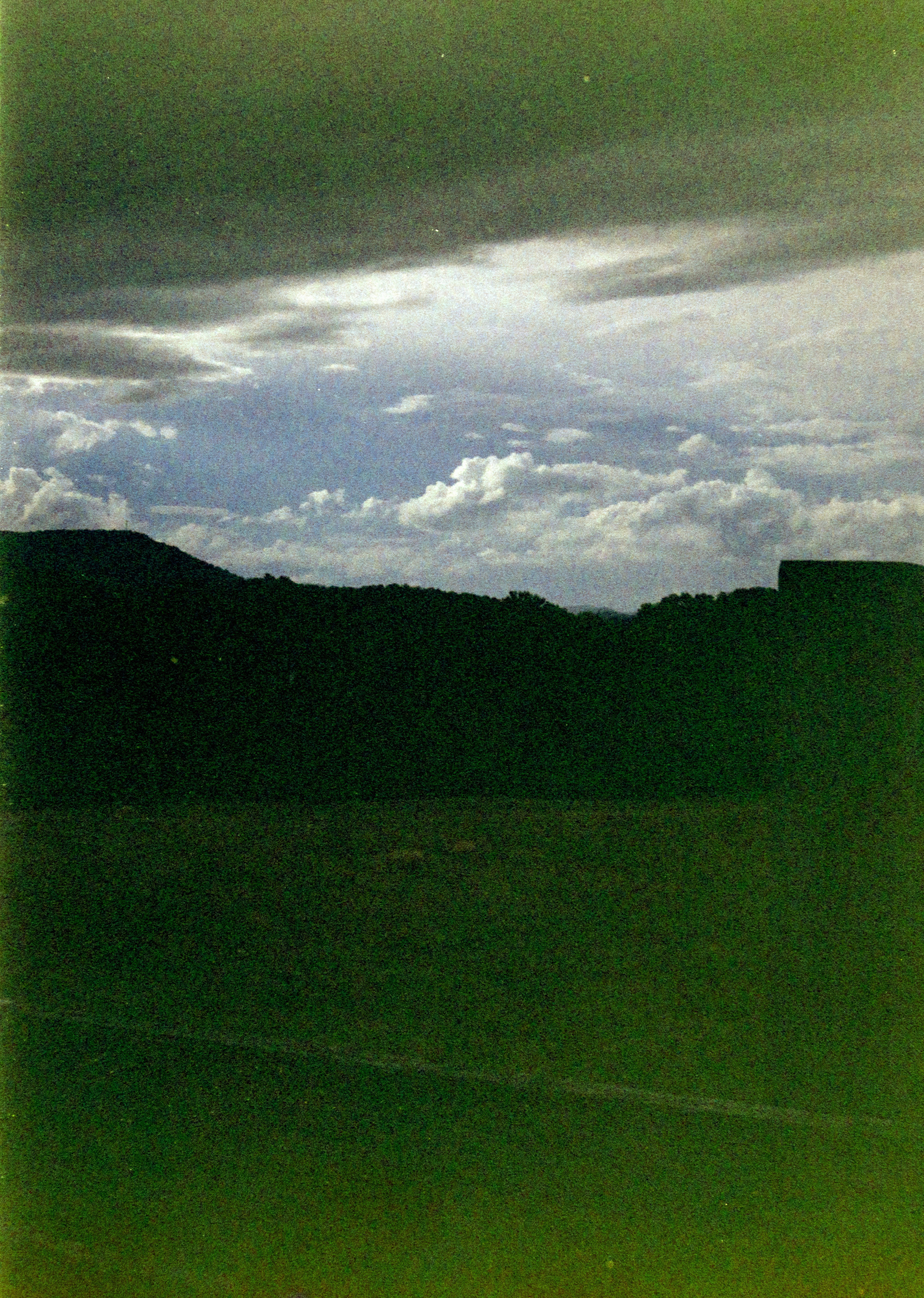 Dark clouds gather over a green landscape.