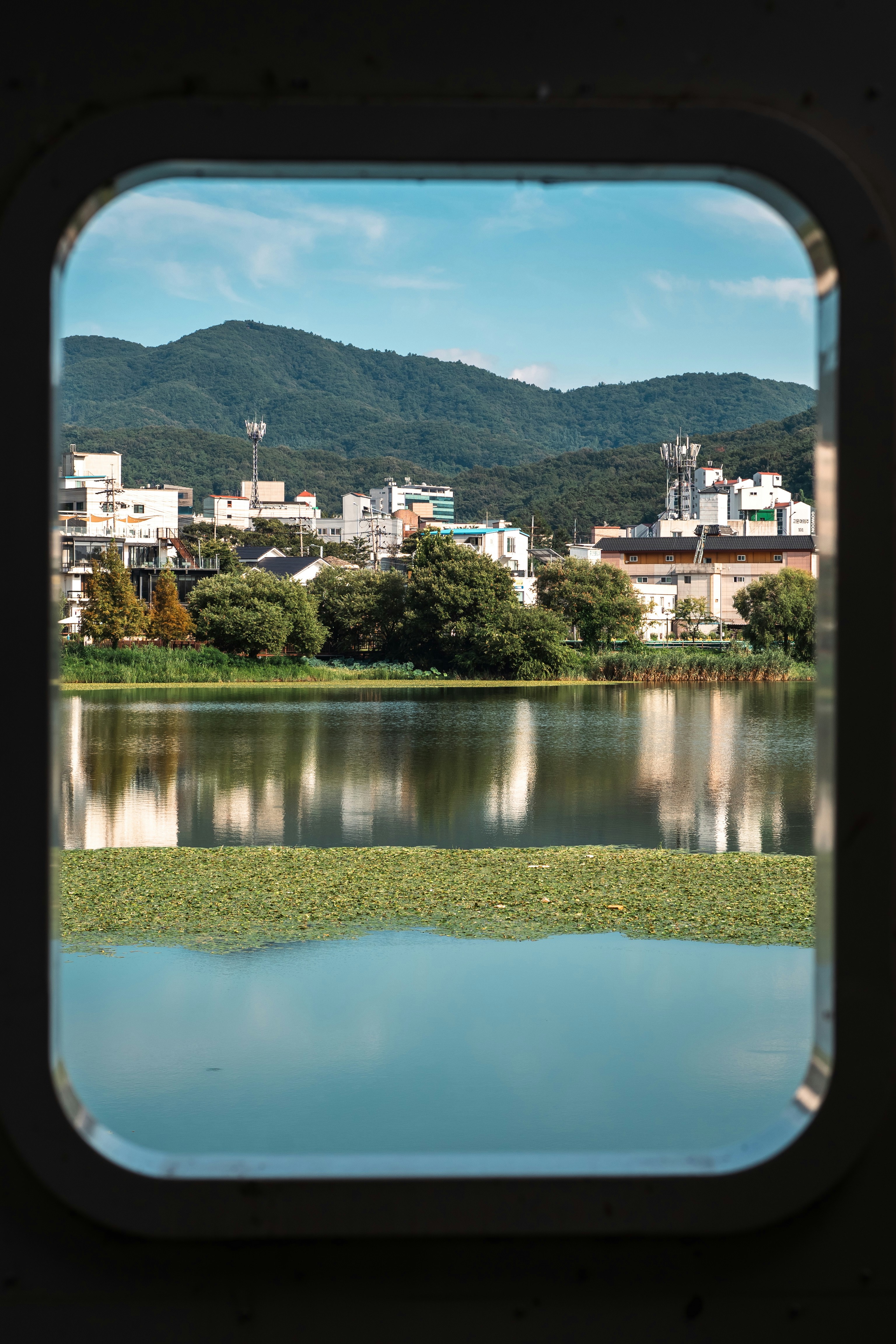 Cityscape reflected in a calm lake with mountains behind.