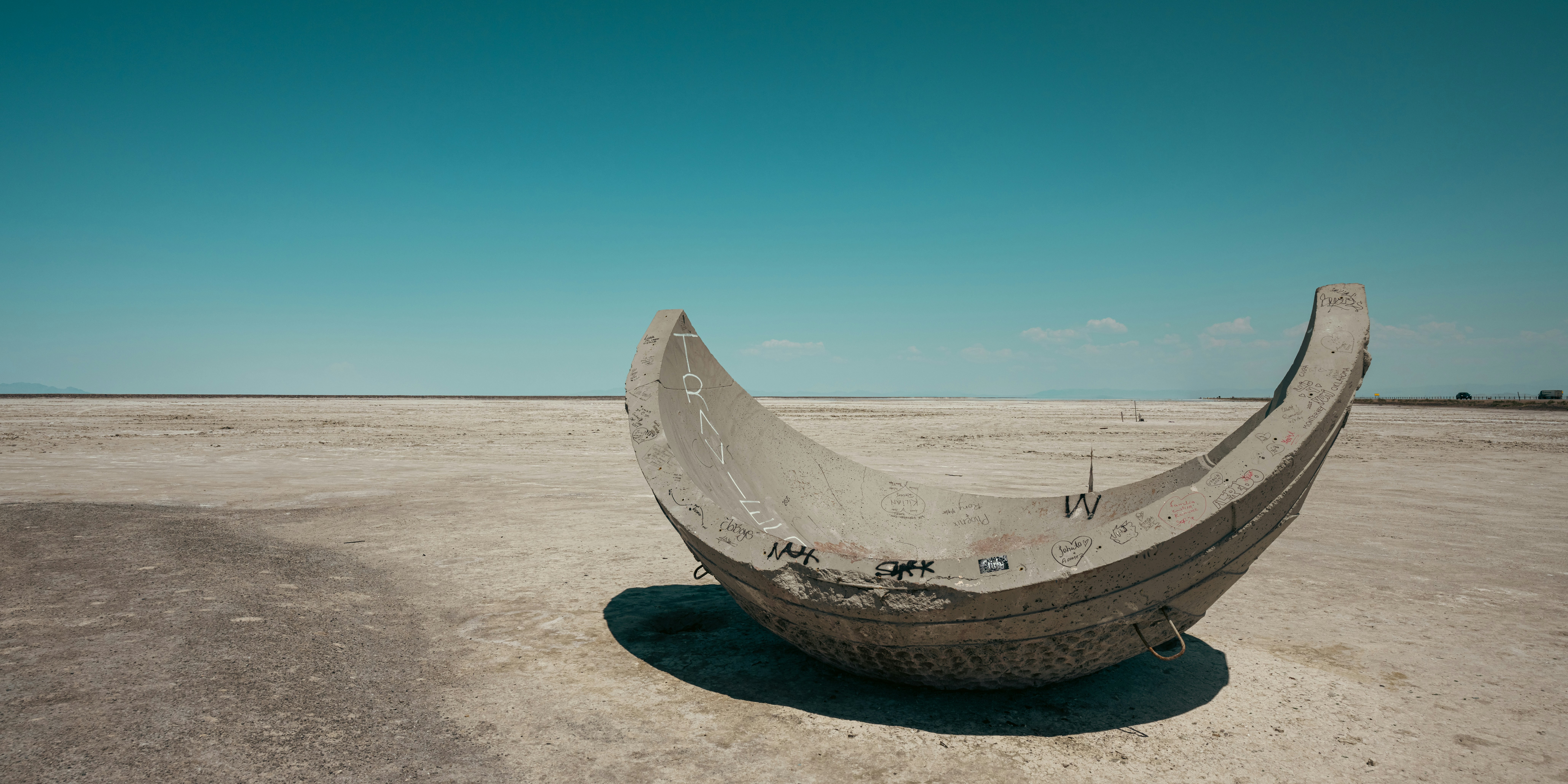 A weathered concrete boat sits alone on a vast, arid landscape under a clear blue sky.