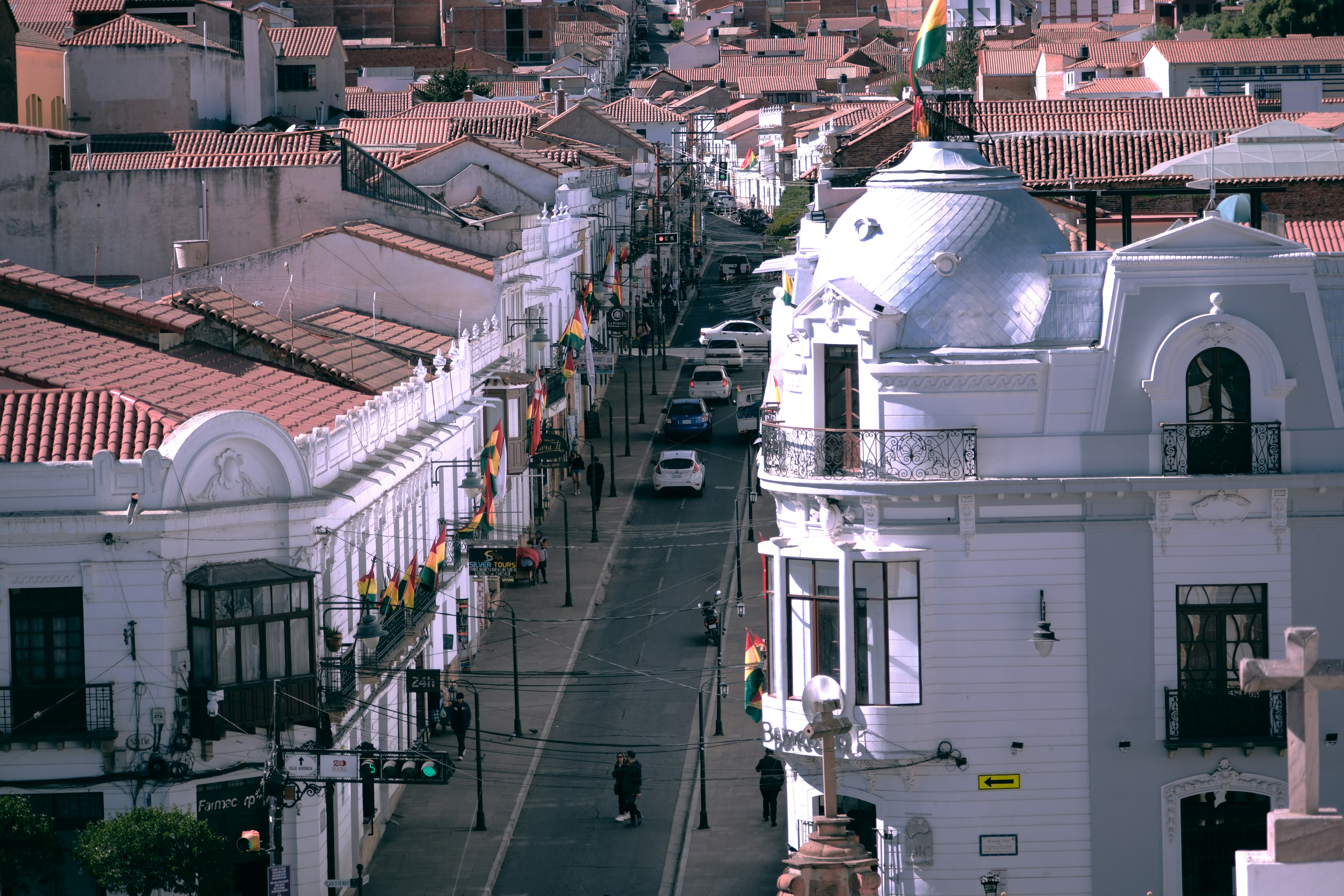 Street view of colonial buildings with cars and people.