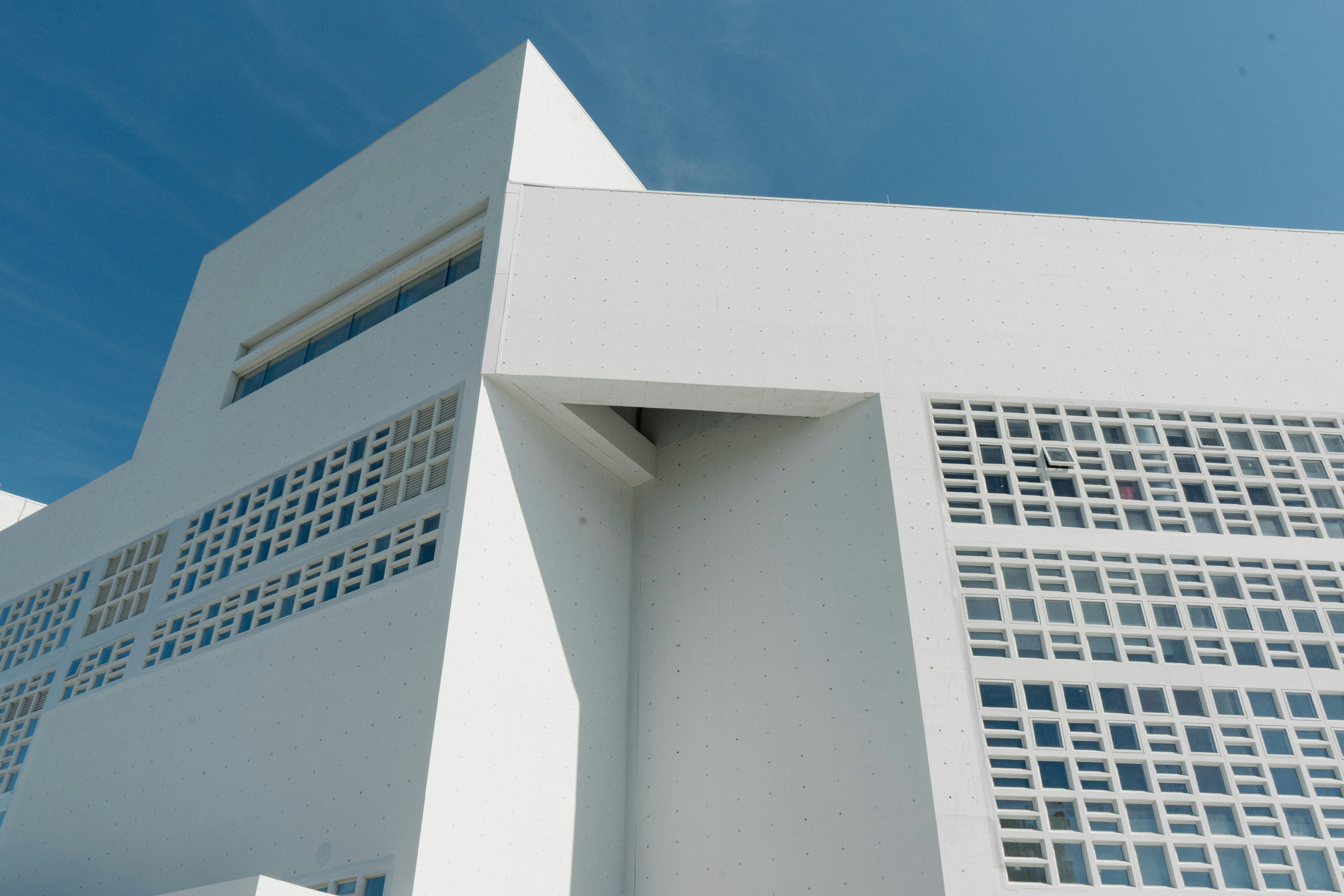 Modern architectural design featuring a striking white facade with geometric patterns and large windows. The interplay of light enhances the building's unique features.
