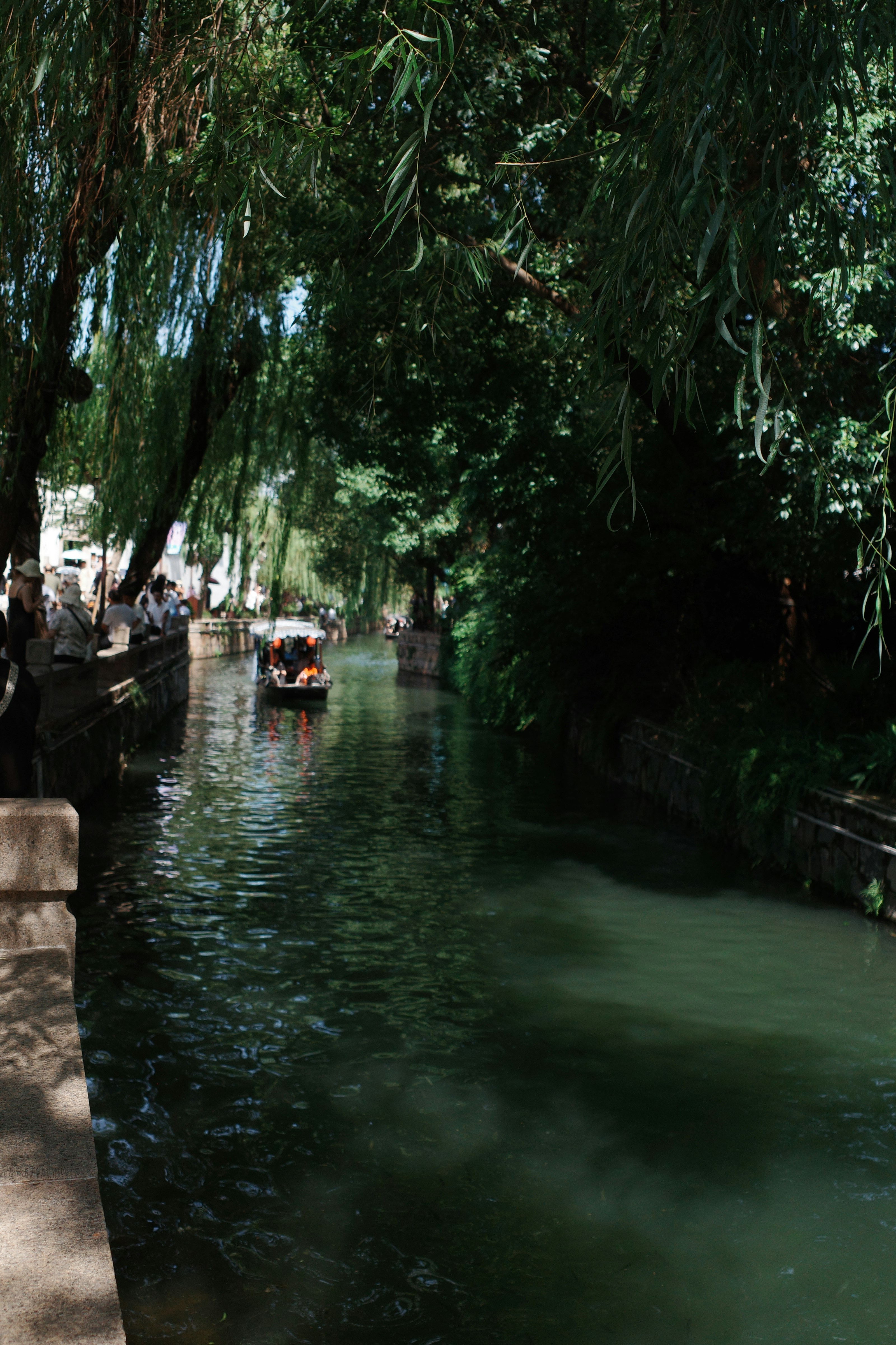 Boat on a tree-lined canal with people on shore
