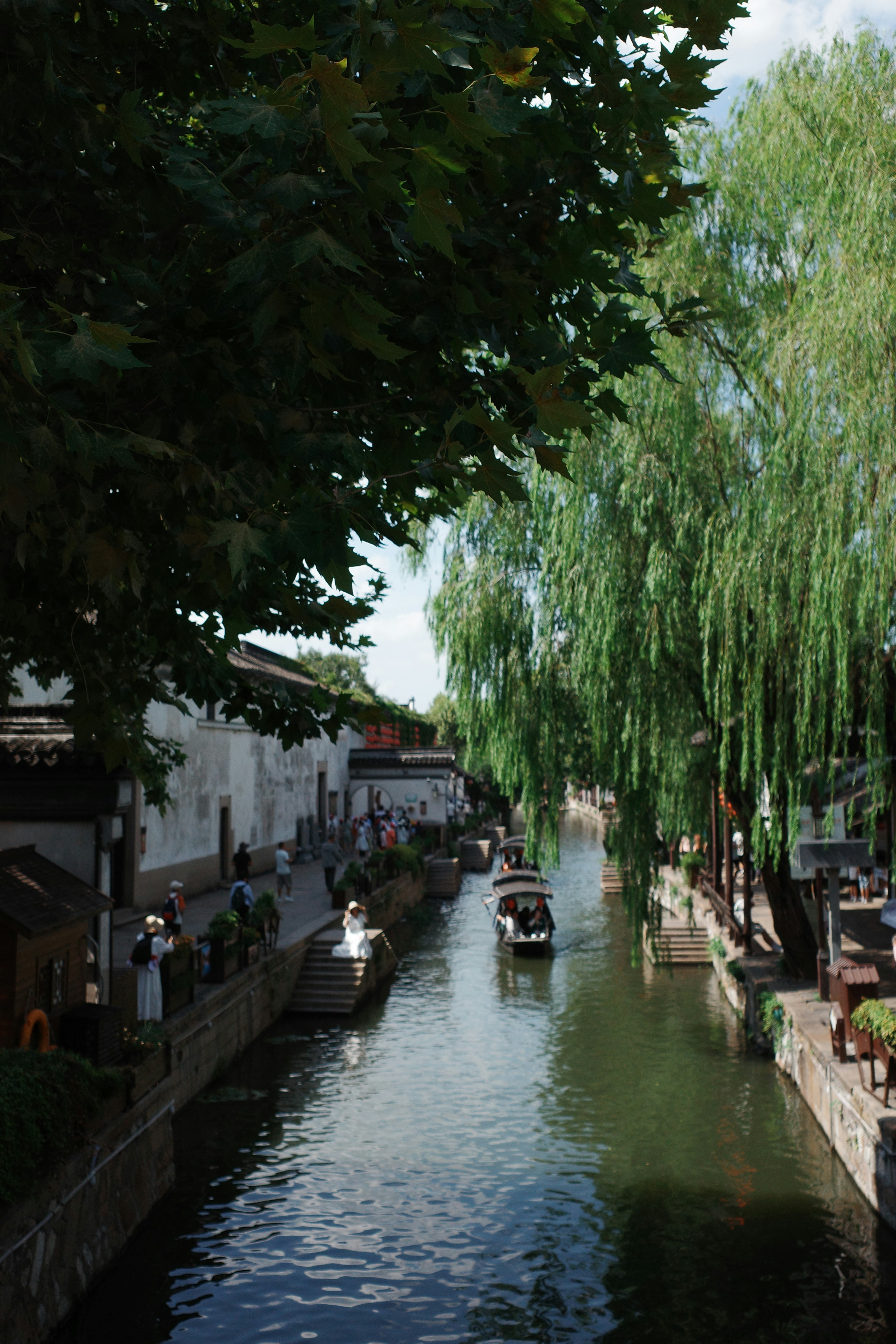 Boats travel down a narrow canal lined with trees.