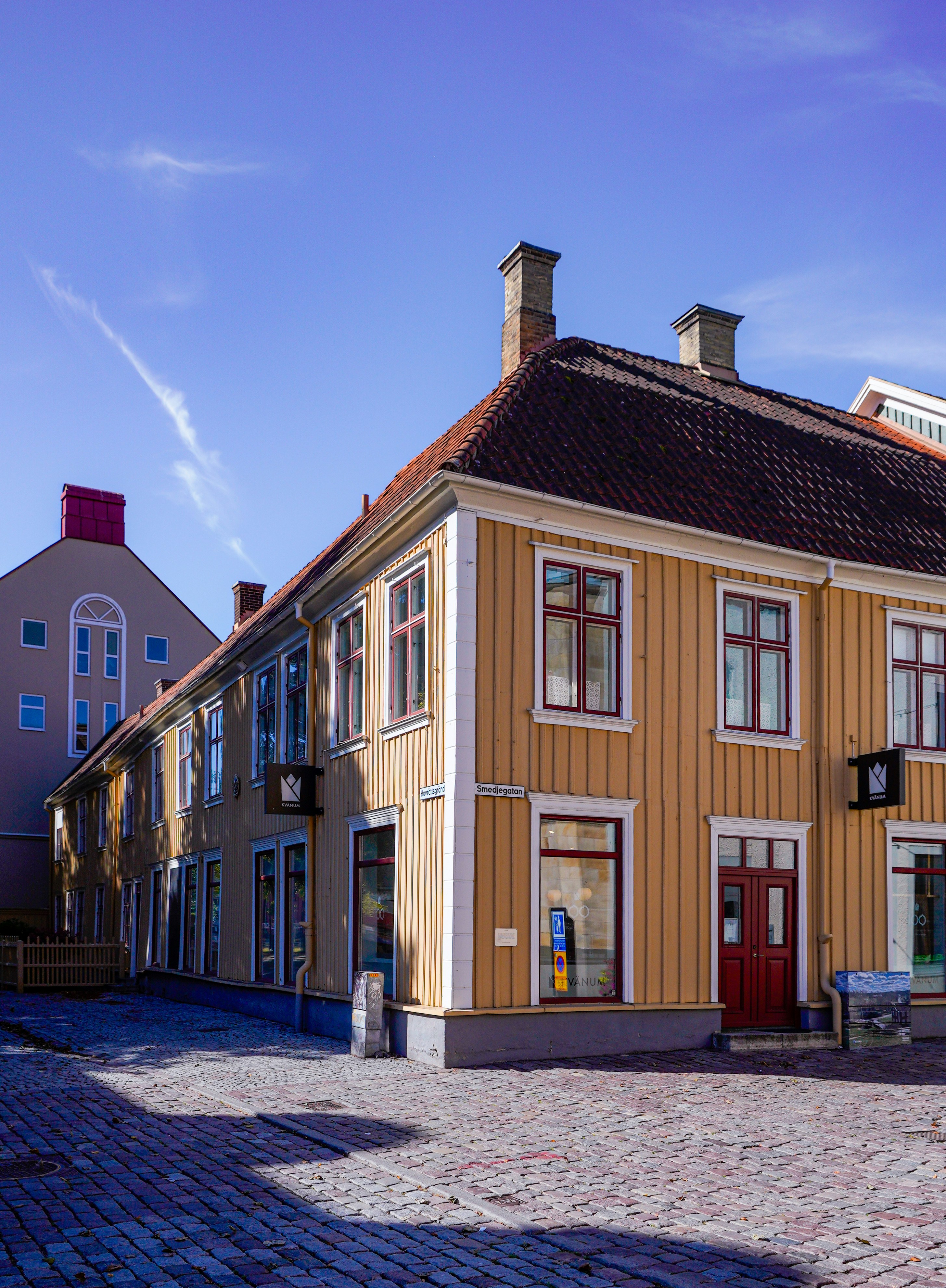 Yellow wooden building with red doors on cobblestone street.