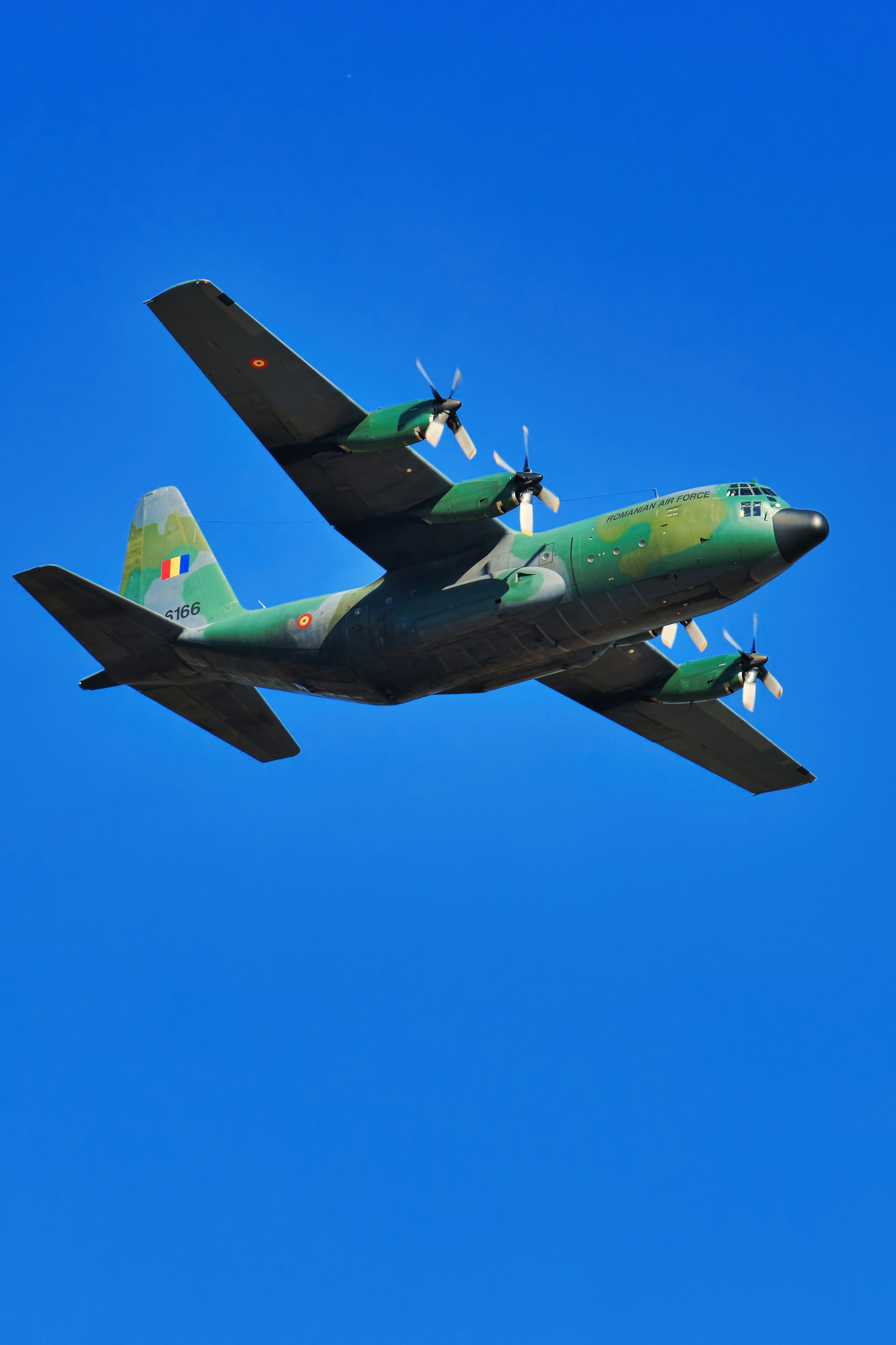 Emerald camo C-130 Hercules slicing through a sapphire sky