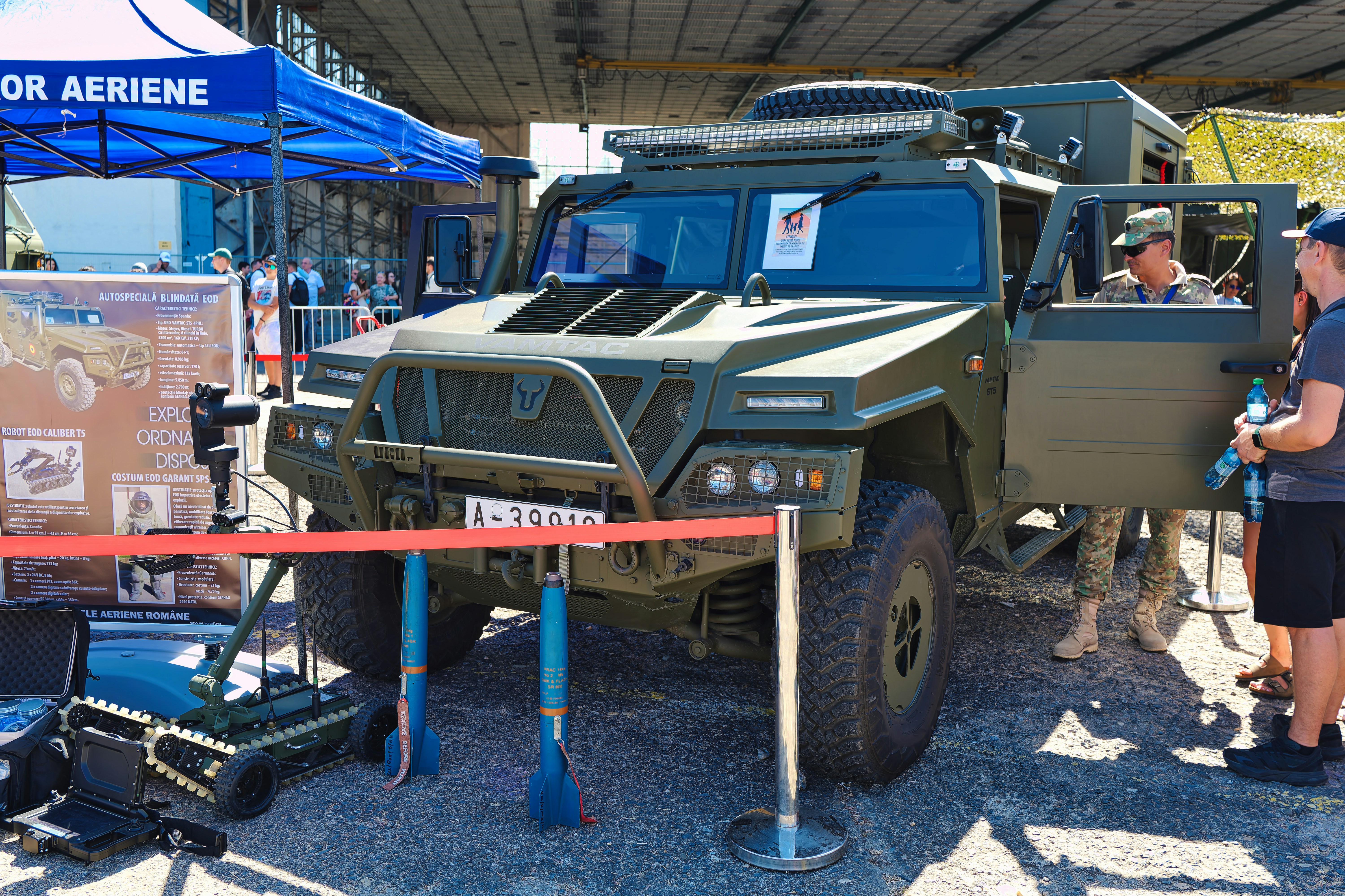 A tactical military vehicle showcased at an exhibition, surrounded by informational displays and engaged visitors. The vehicle's robust design highlights modern military capabilities.