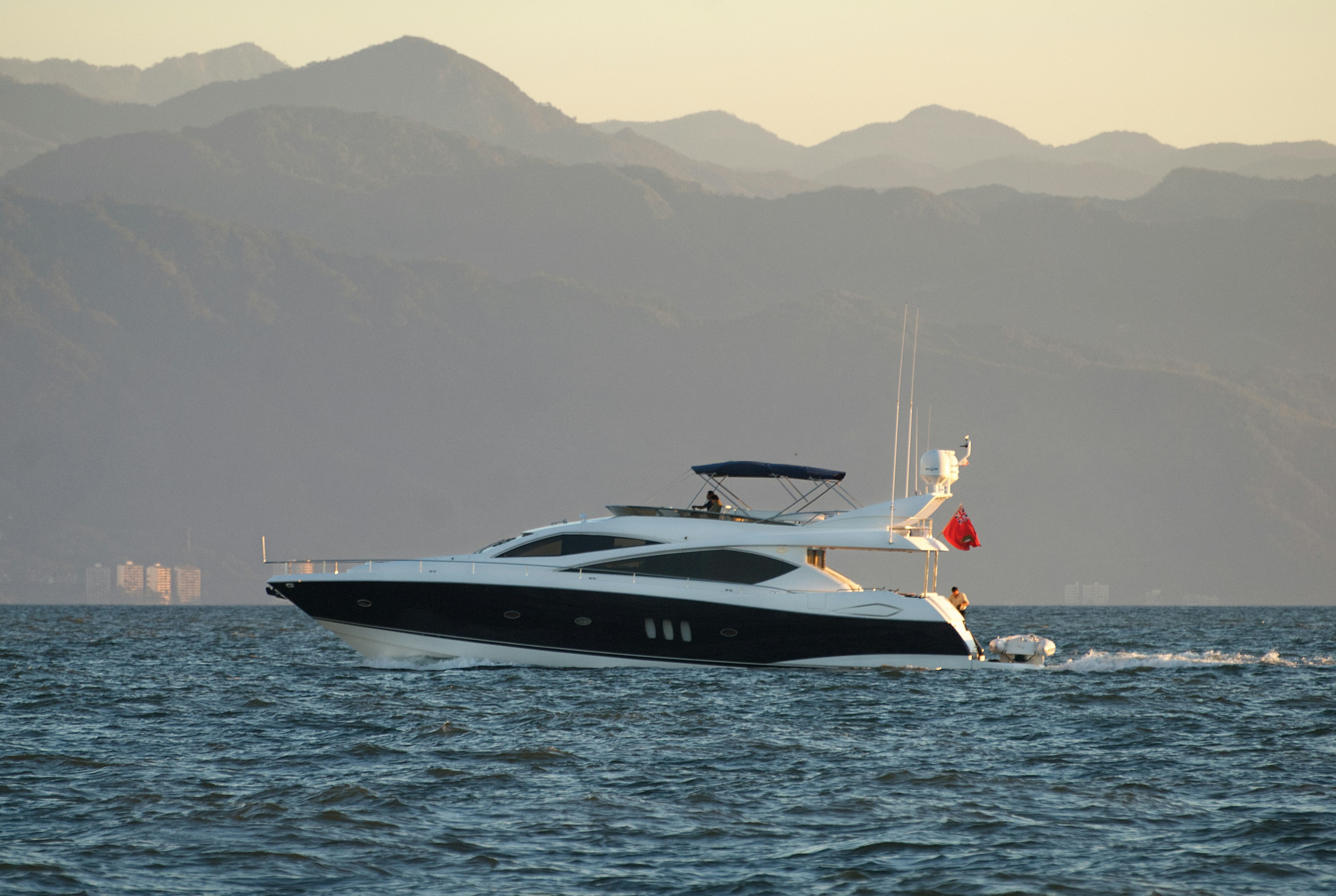 A motor yacht navigating at dusk | A sleek yacht sails on the ocean with mountains behind.