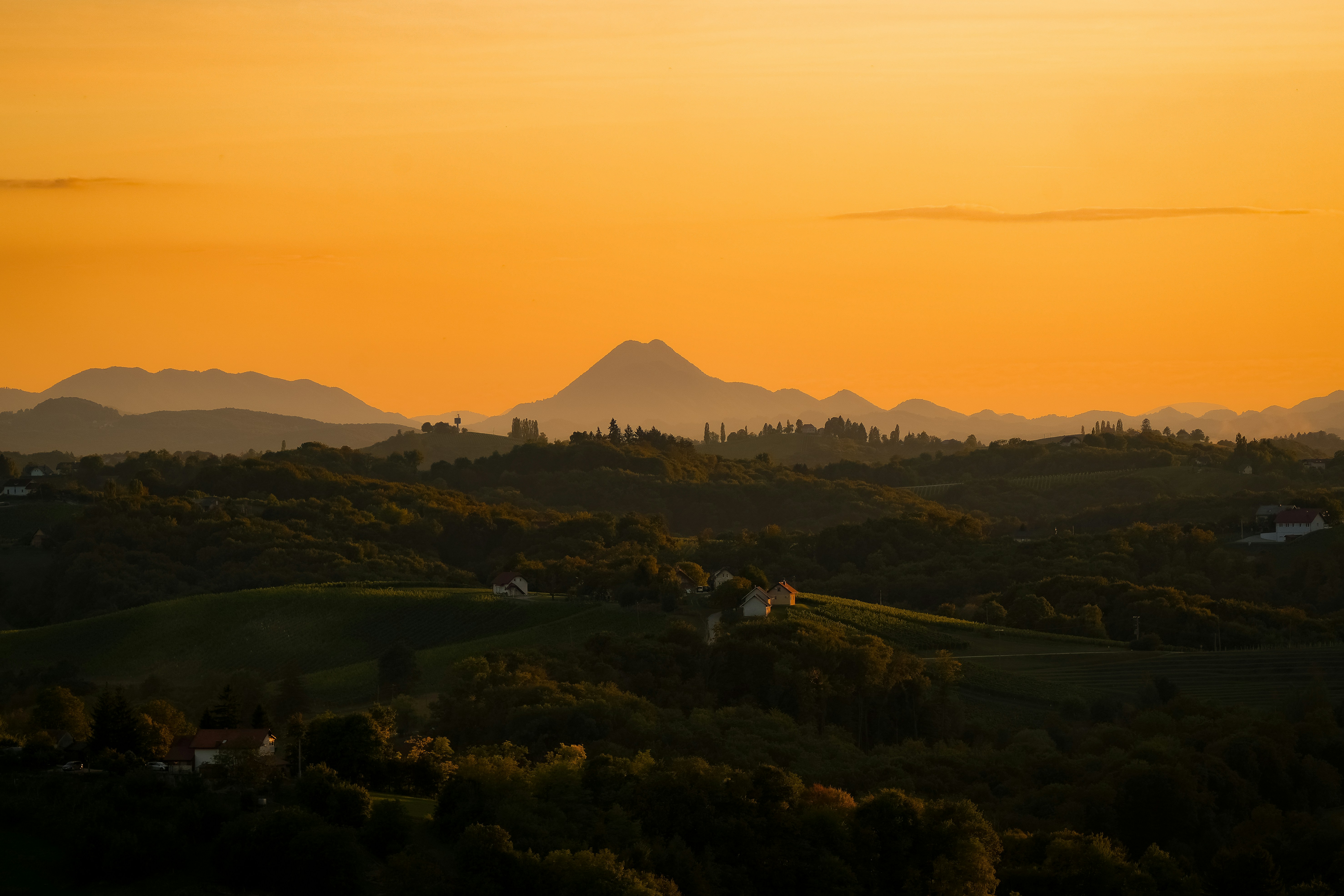 Vast landscape of rolling hills under a warm golden sky, with a distant mountain silhouette creating a serene backdrop.