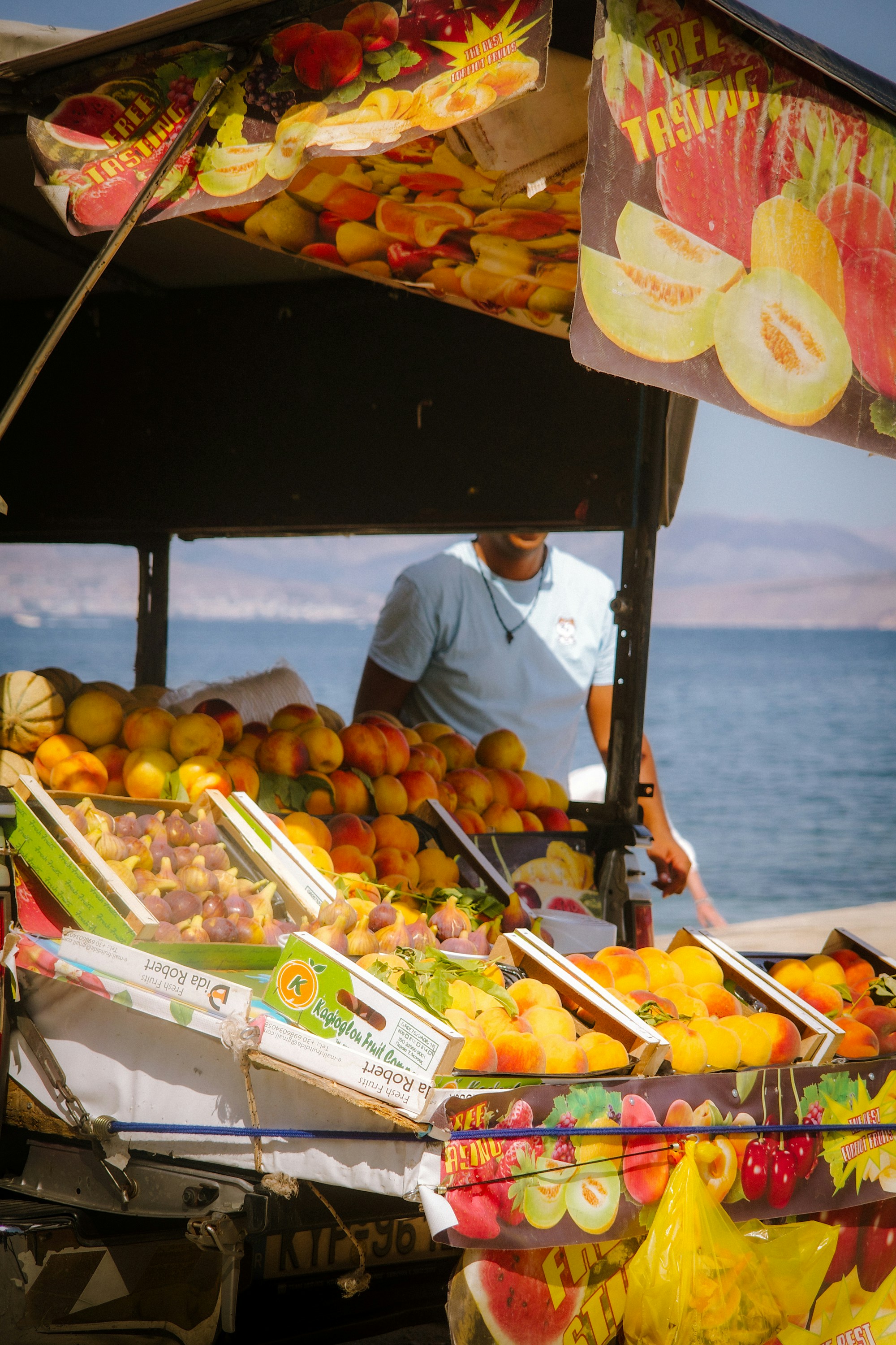 Sunlit Seaside Fruit Cart: Crates of Peach and Citrus Framed by a Casual Vendor