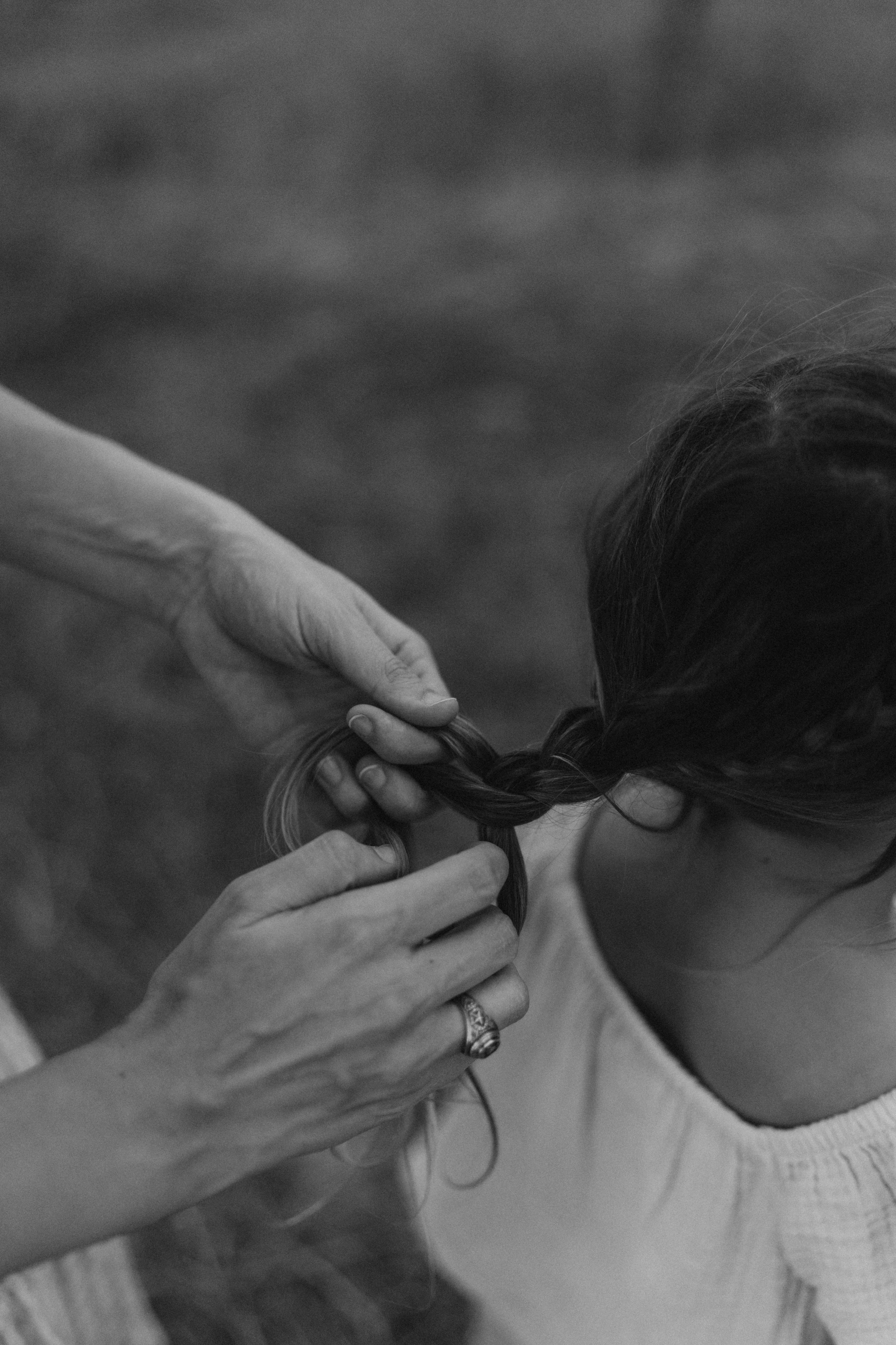 Hands braiding dark hair in a field