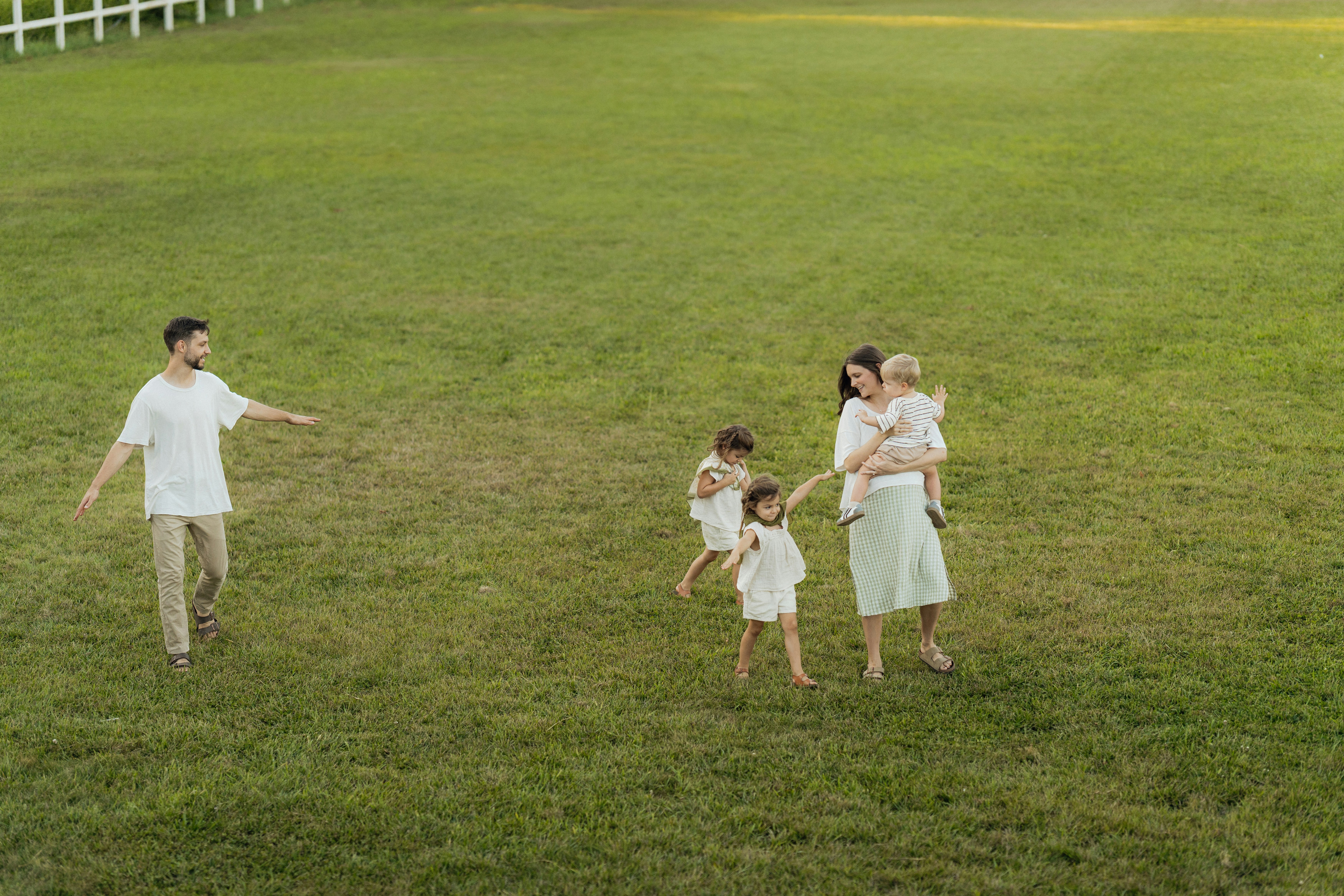 A family enjoys a leisurely walk in a lush green meadow, with children playing and a parent carrying one child. The scene captures a moment of togetherness and joy.