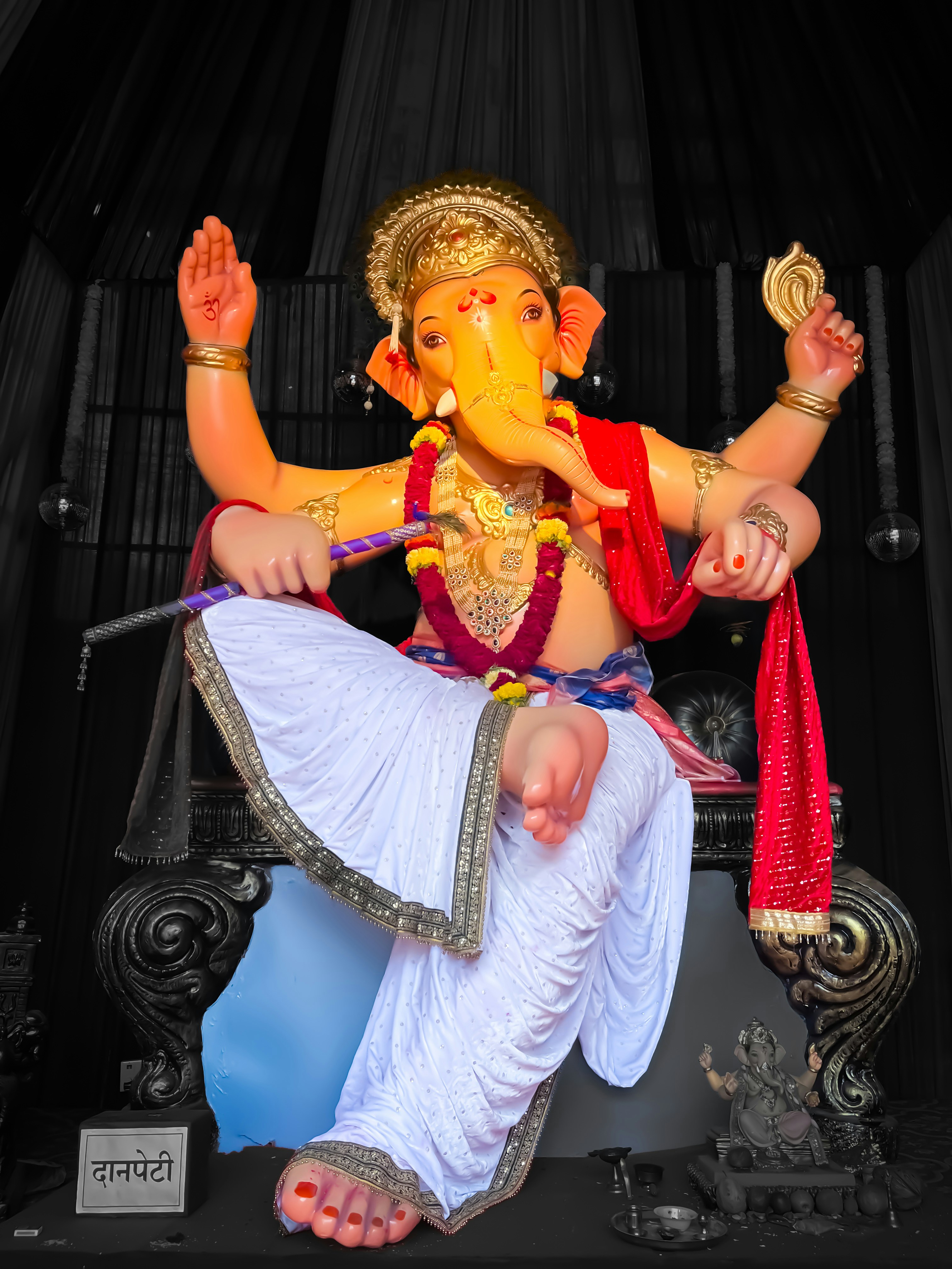 Vibrant idol of Lord Ganesh adorned with intricate jewelry and a traditional white garment, seated gracefully against a dark backdrop.