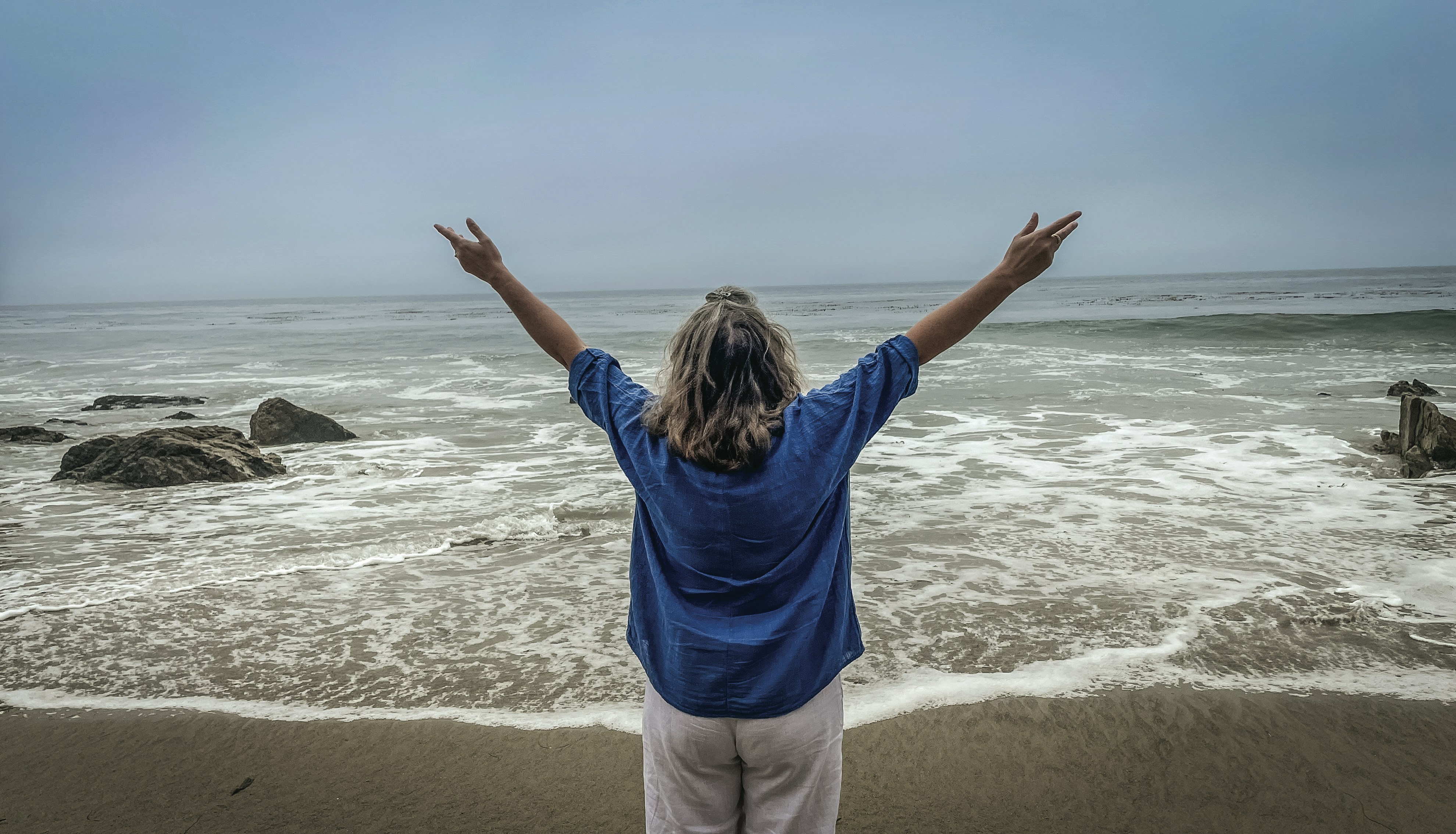Woman with arms raised on a beach facing ocean photo – Free Worship ...