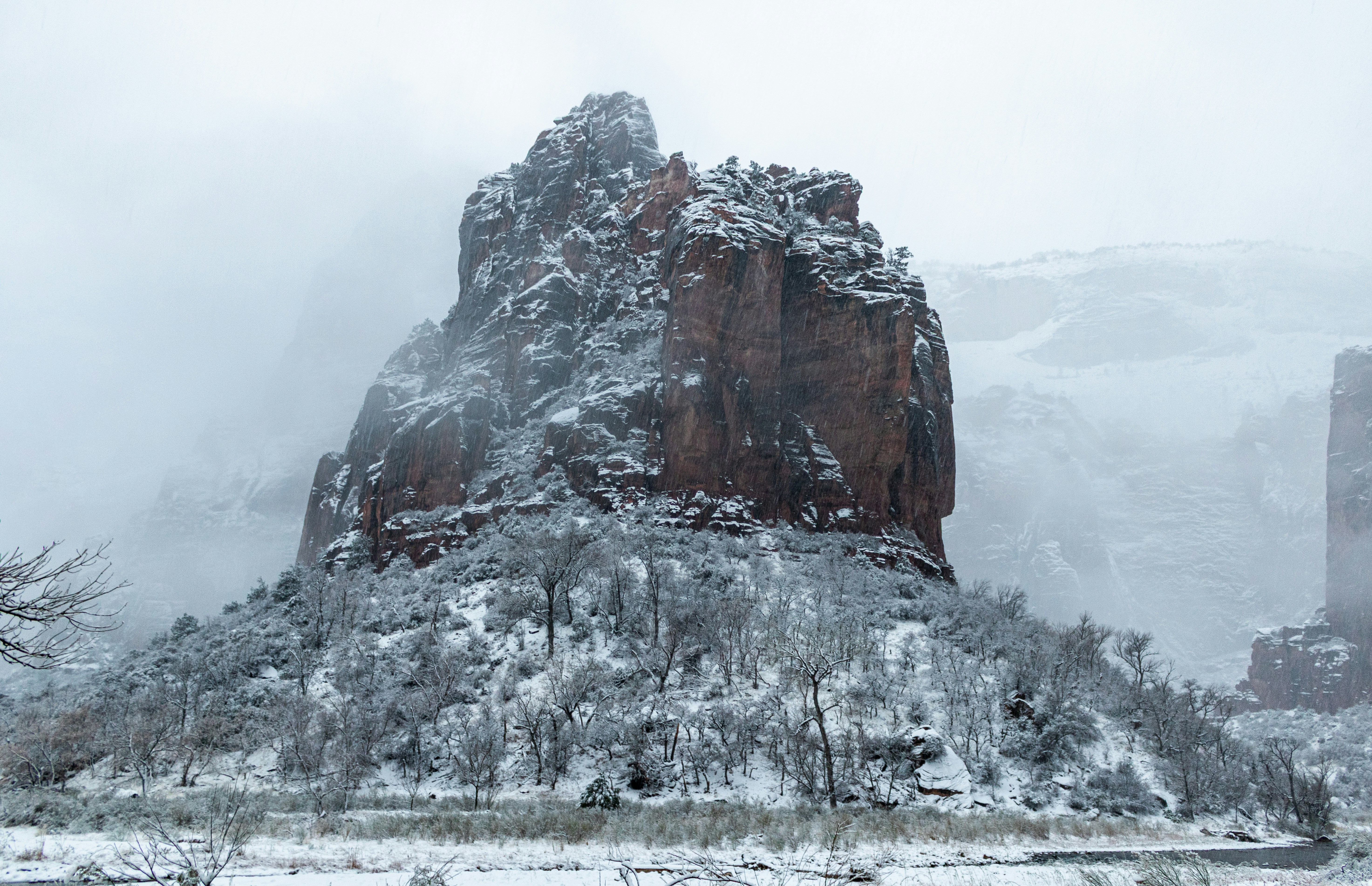 A majestic rock formation shrouded in snow, surrounded by a barren landscape under a cloudy sky.