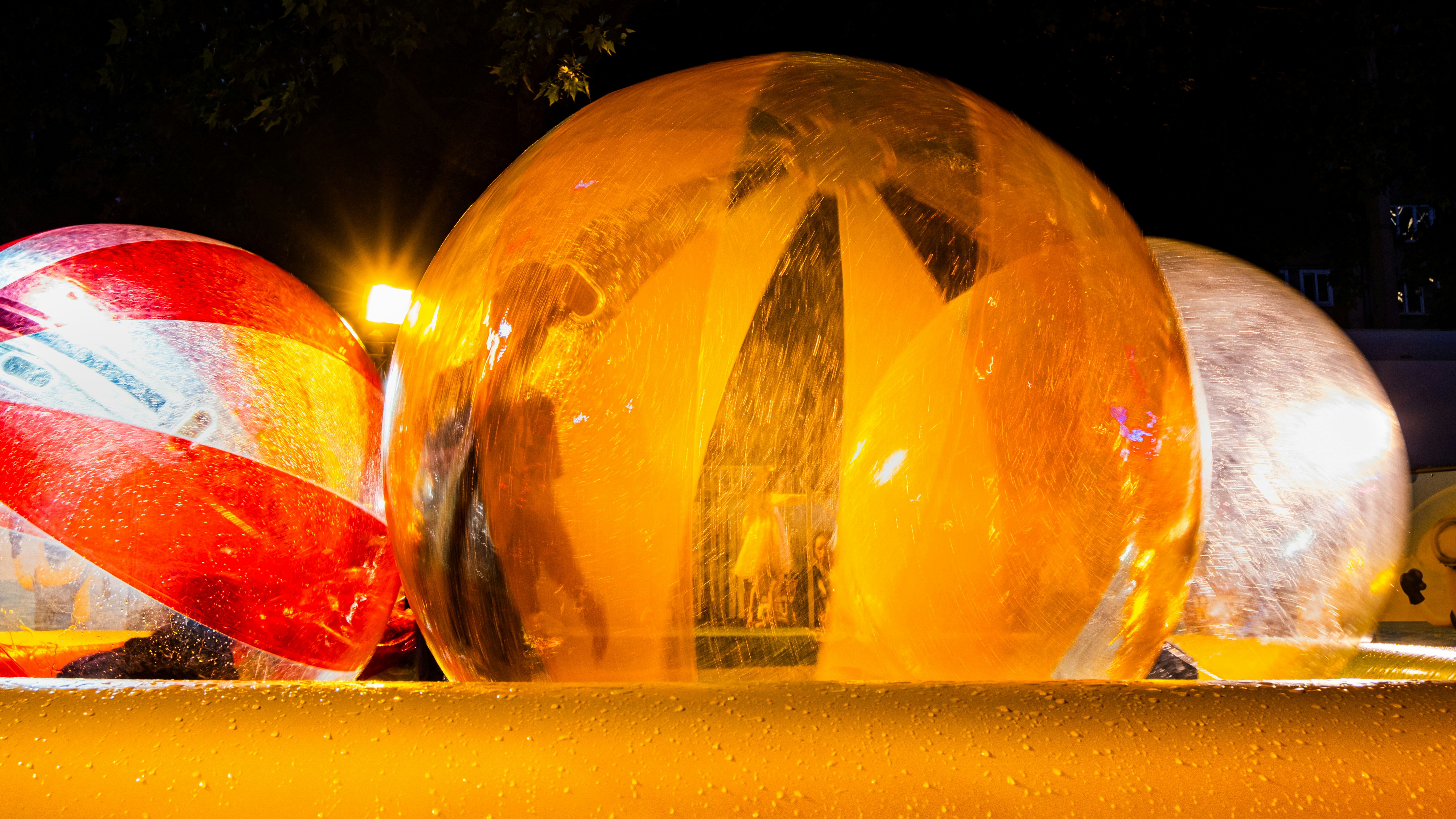 Vibrant illuminated spheres float in a water feature, reflecting colors and creating a playful atmosphere at night.