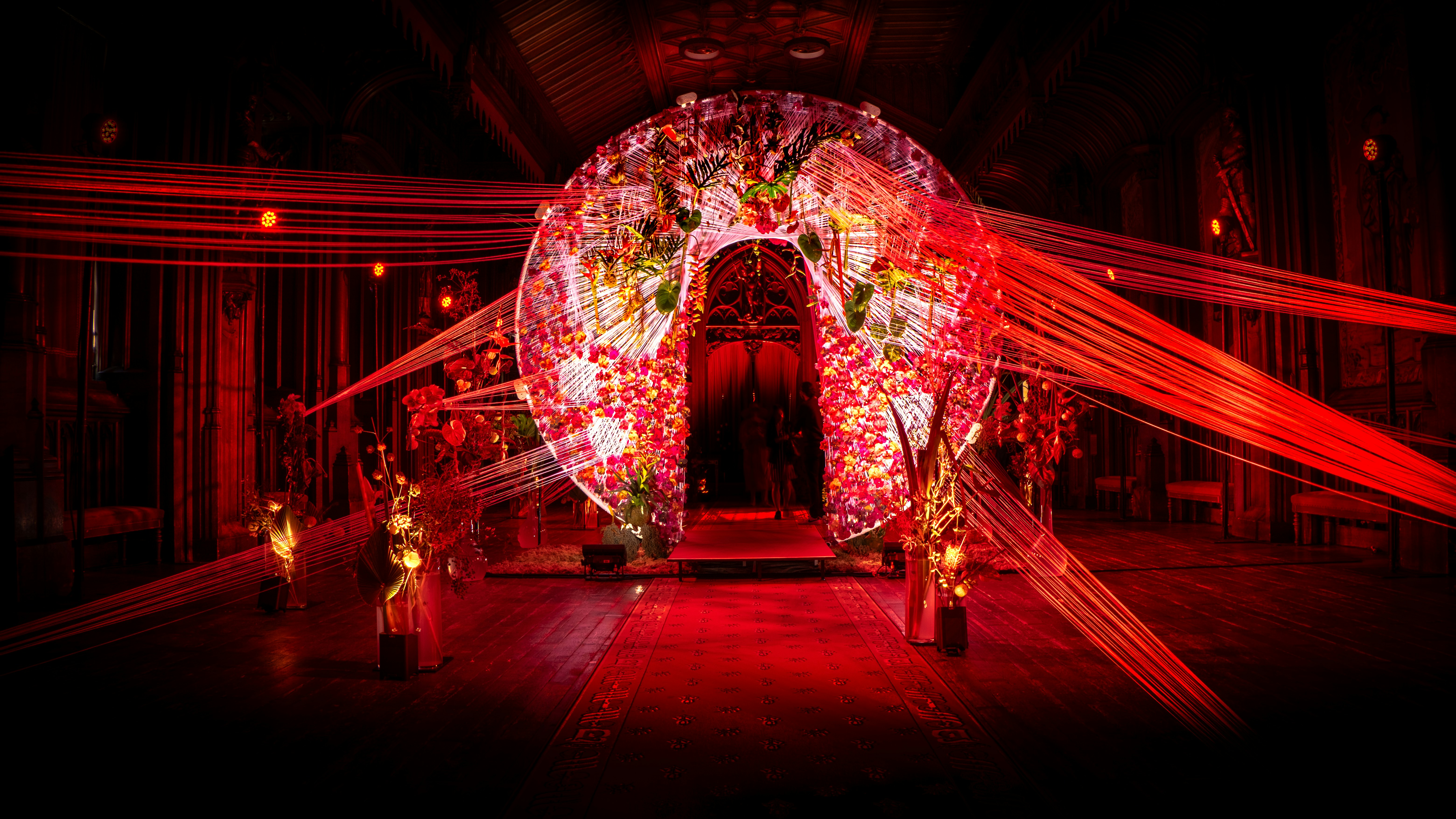 A vibrant installation featuring a floral archway surrounded by dynamic light streaks, creating an immersive atmosphere. The scene invites viewers into a world of art and creativity.