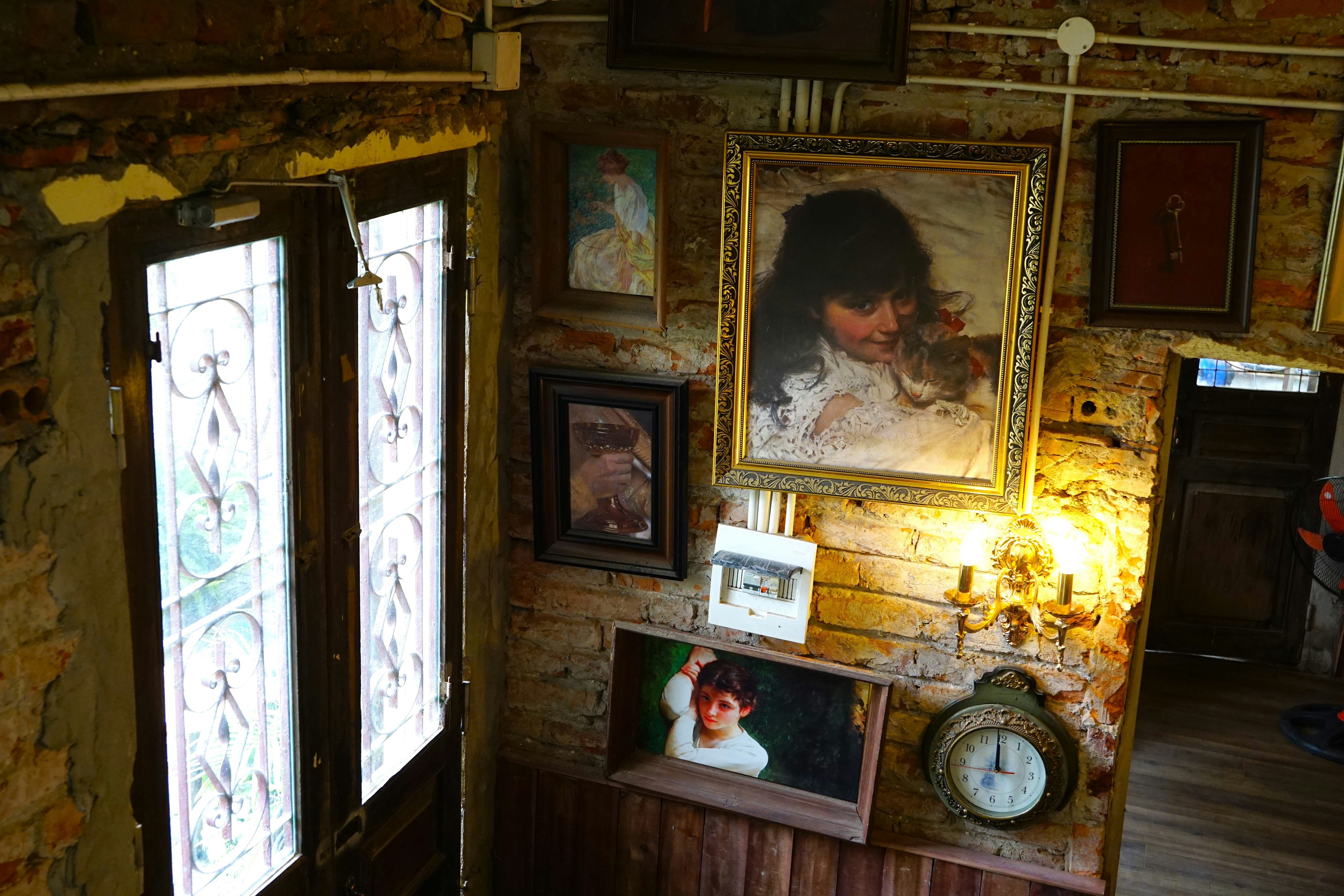 A collection of framed portraits and artwork adorns a rustic wall, illuminated by warm light, creating an inviting atmosphere. The scene captures the essence of a cozy, artistic space.
