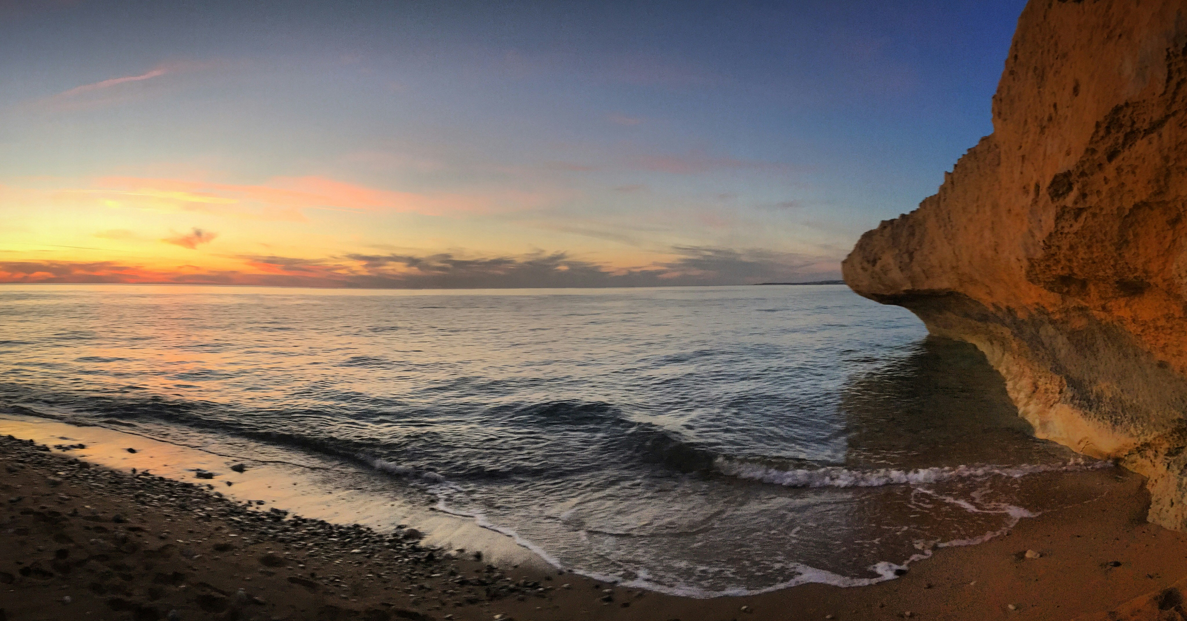 Sunset over the calm Mediterranean sea with a rocky cliff in the foreground, Lémpa, Paphos, Cyprus, October 2018 | Calm ocean waves lap a rocky shore at sunrise.