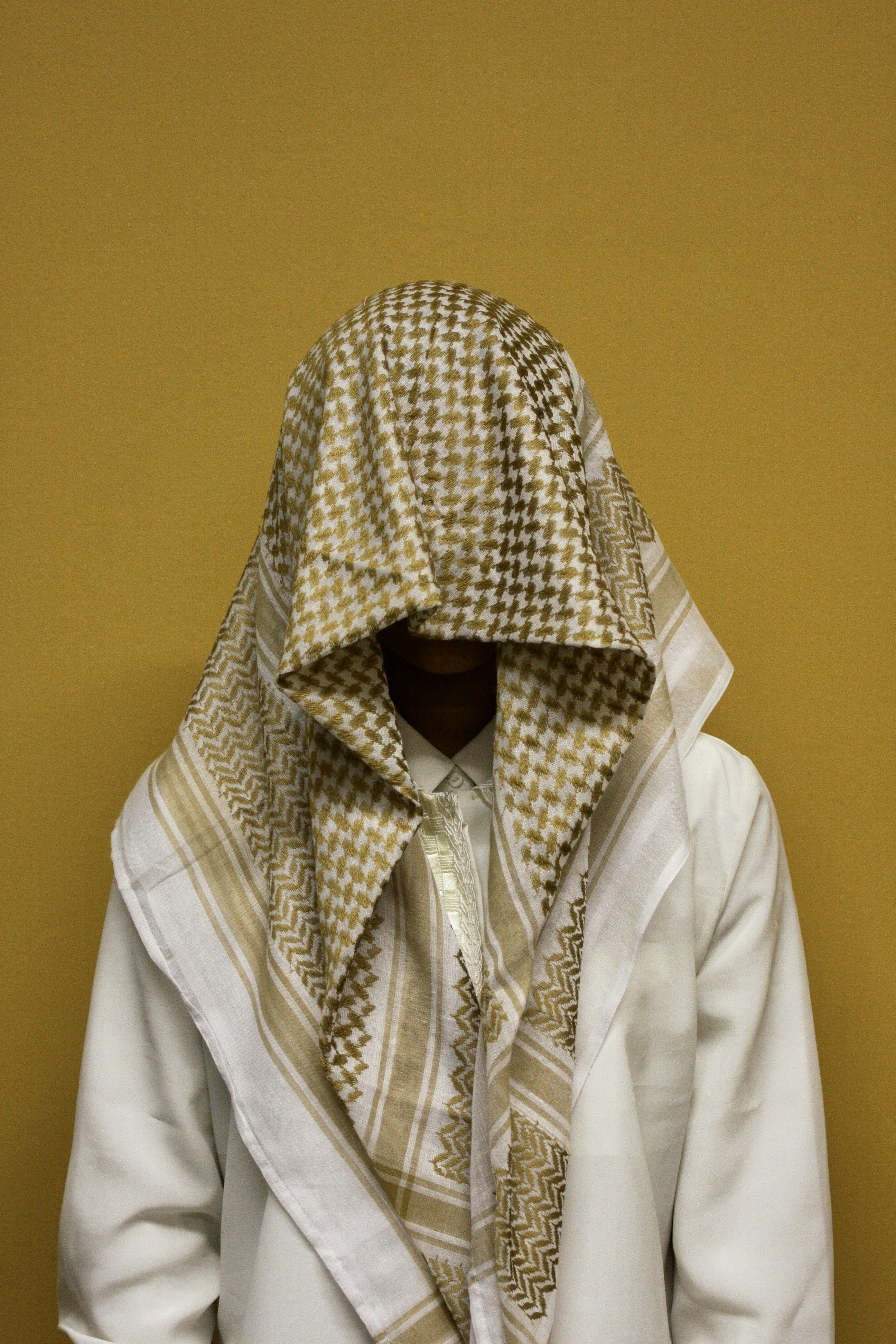 Person in traditional middle eastern attire against yellow wall.