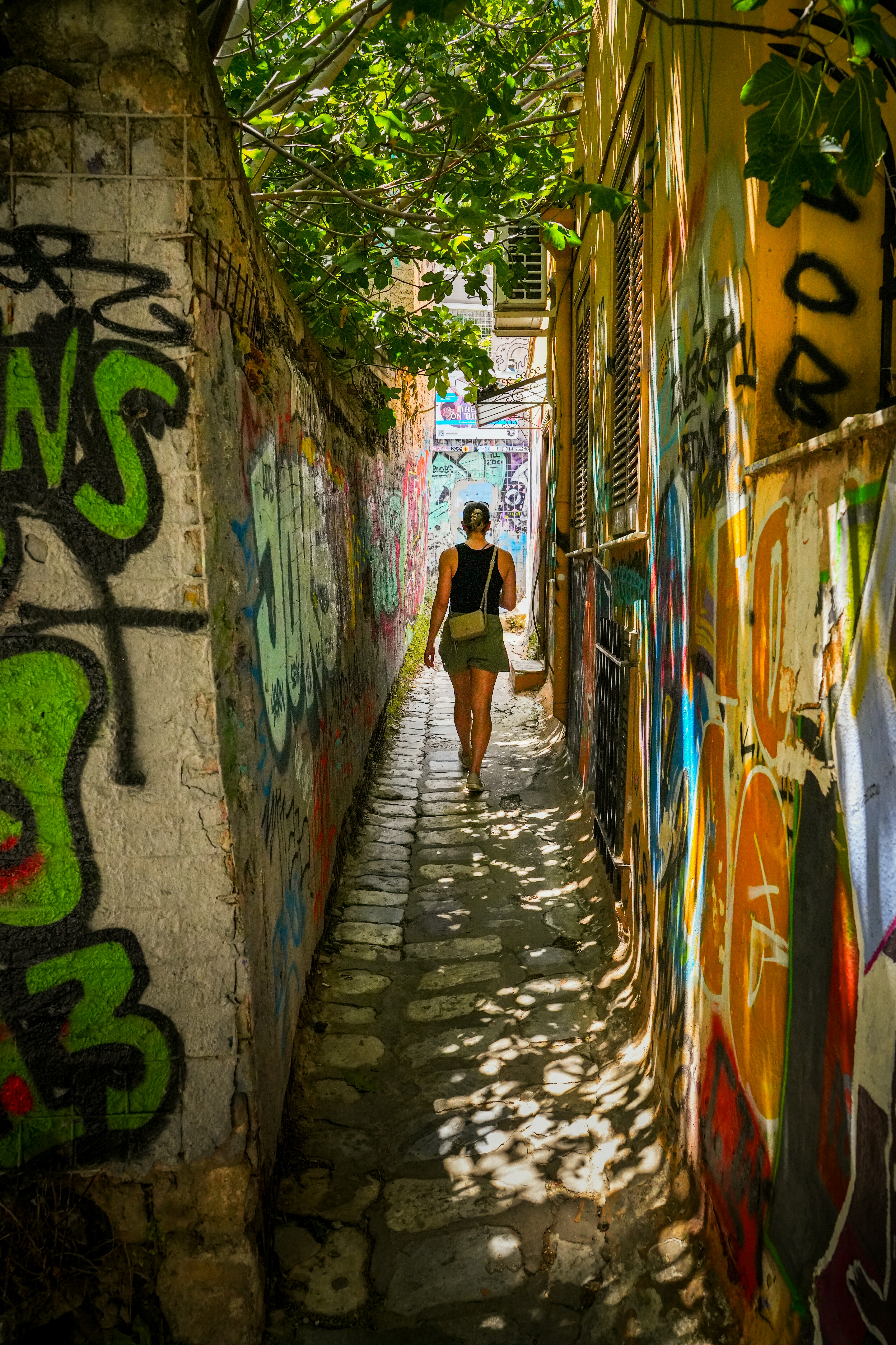 An alley in the Greece backstreets leading to Anafiotika - a quaint, scenic neighborhood in the heart of Athens. | Woman walking down a graffiti-covered alleyway