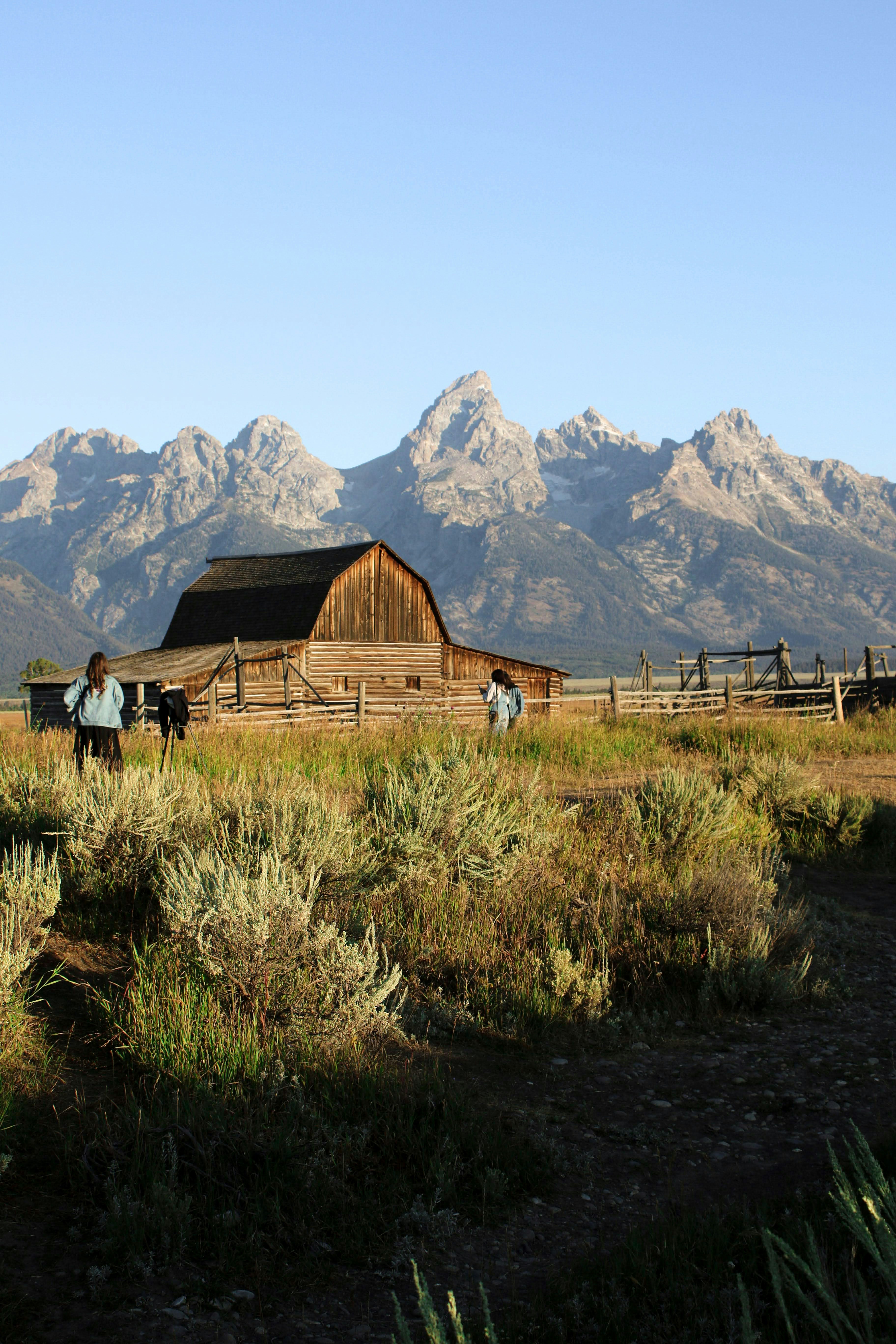 Historic barn nestled in a grassy field with towering mountains in the background, capturing the essence of the American West.