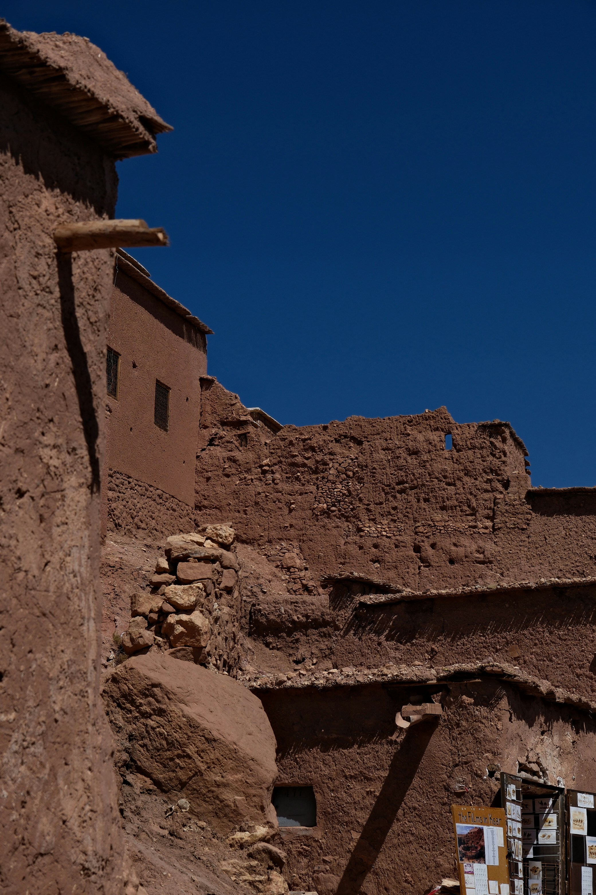 Weathered adobe structures rise against a clear blue sky, showcasing the rich texture of traditional architecture. Informational signage hints at the site's historical significance.