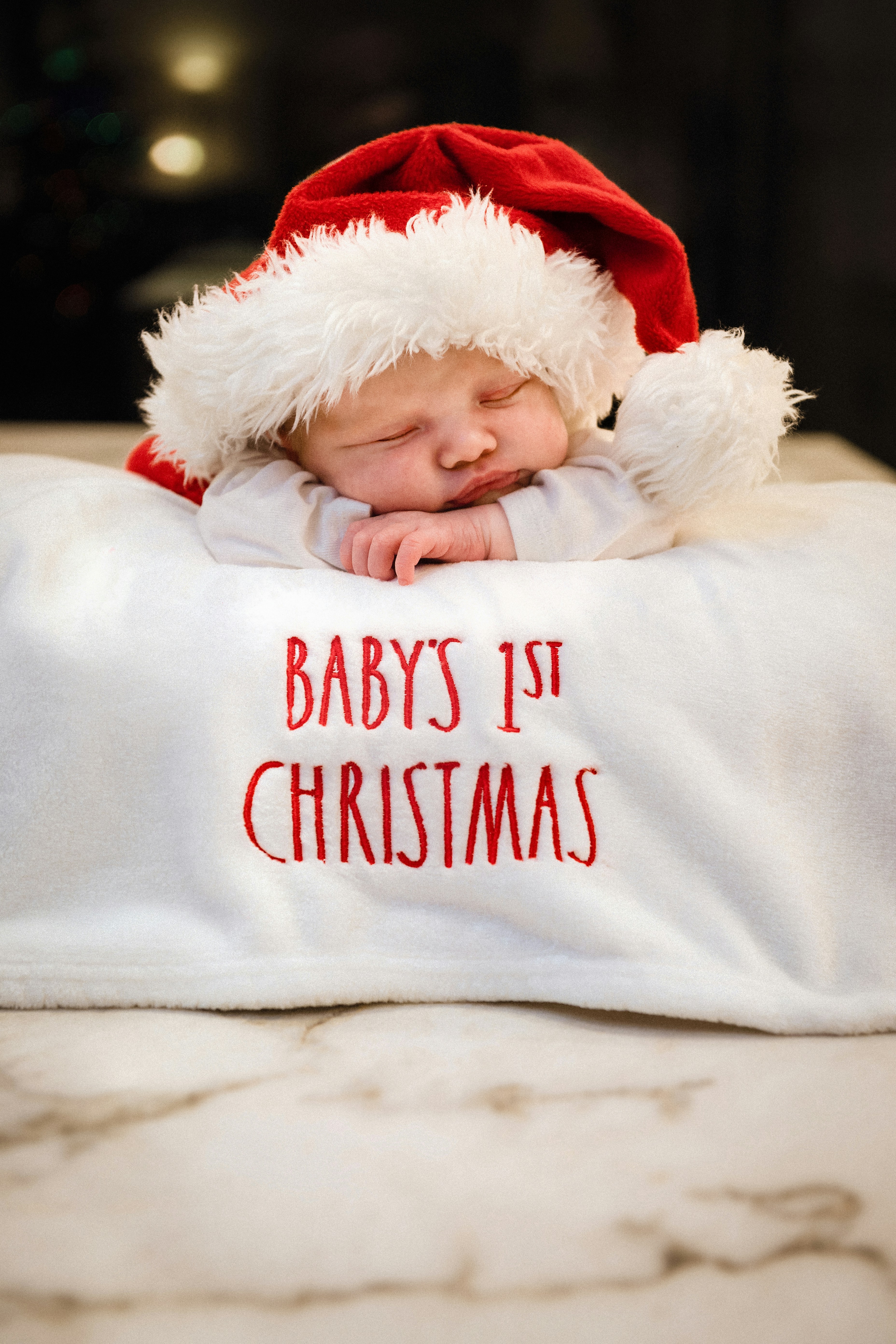 Sleeping Through Christmas | Newborn baby wearing santa hat with 'baby's 1st christmas' blanket.