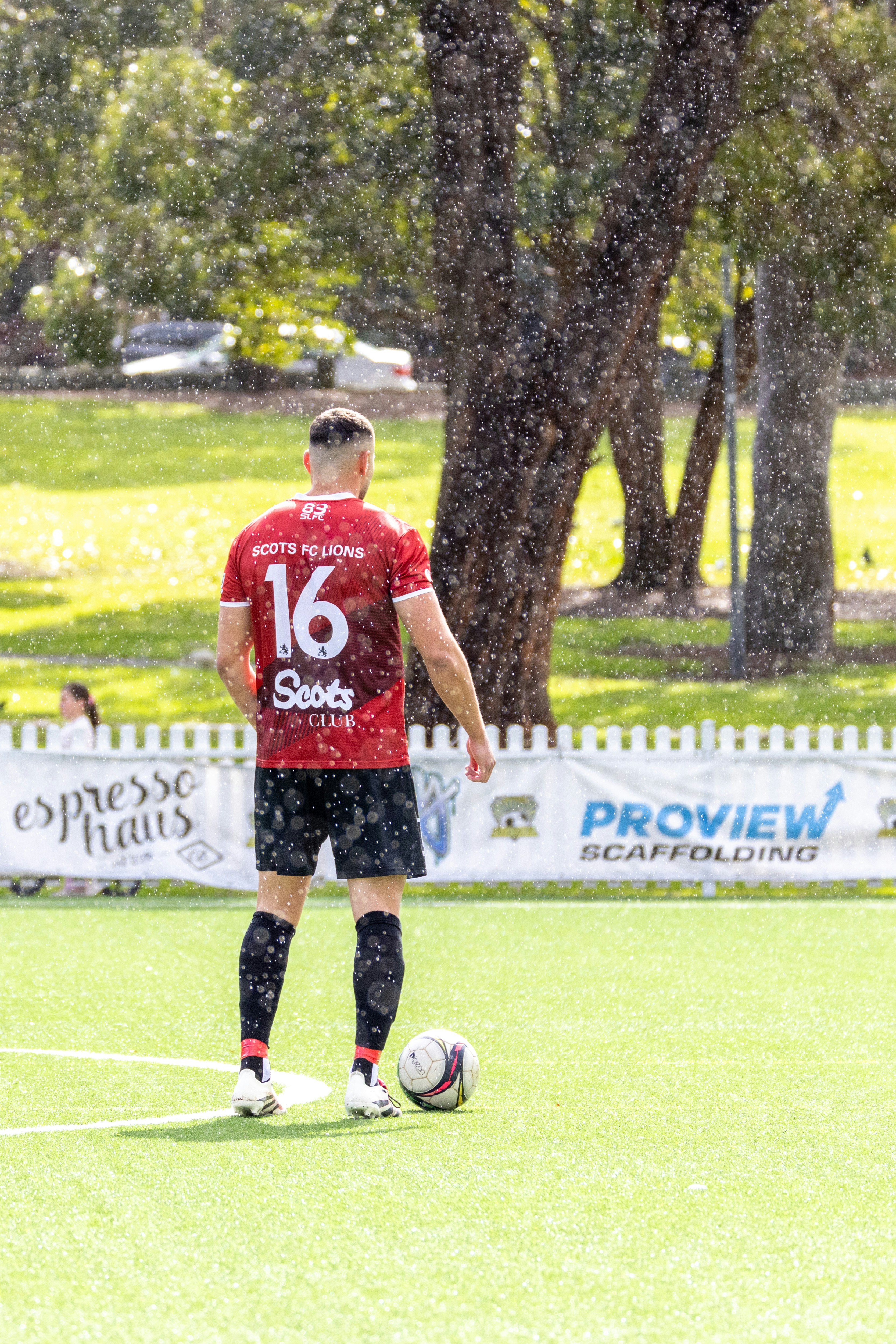 Number 16 Stands with Ball at His Feet on a Sunlit Pitch as Droplets Drift Through the Air