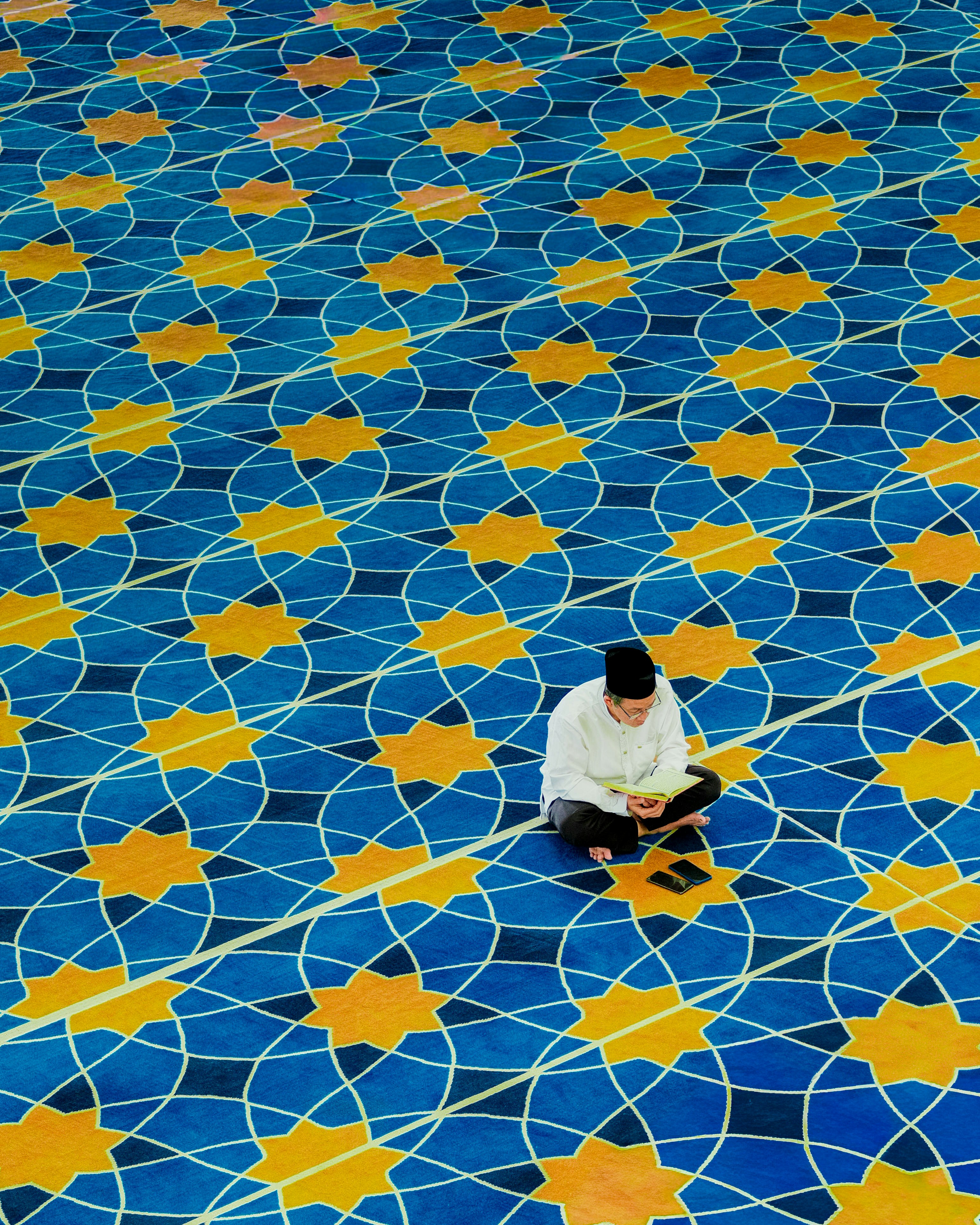 A solitary figure sits cross-legged on a beautifully patterned blue and yellow tiled floor, immersed in contemplation. The intricate design creates a mesmerizing backdrop.