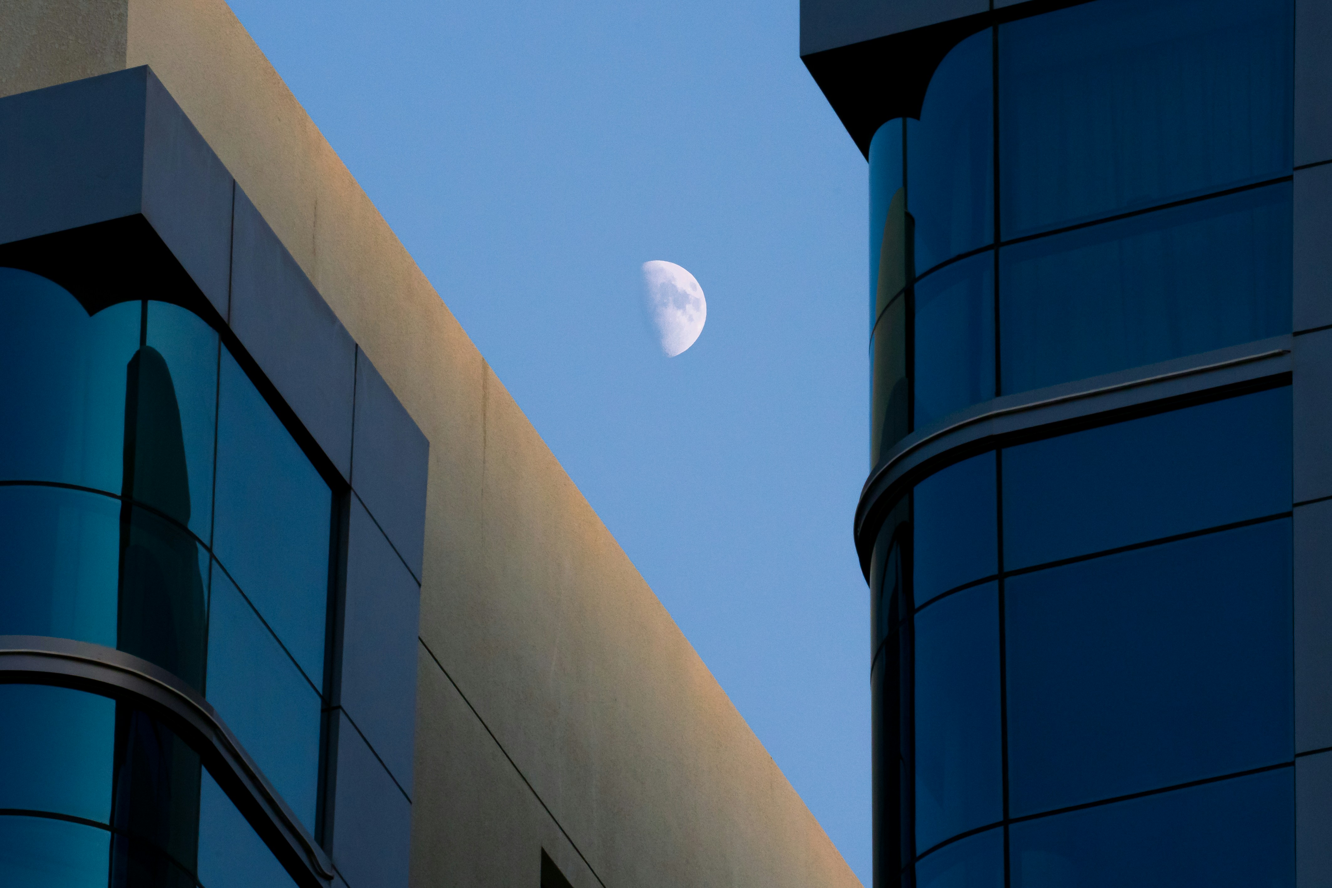 Half moon visible between modern buildings photo – Free Blue Image on ...