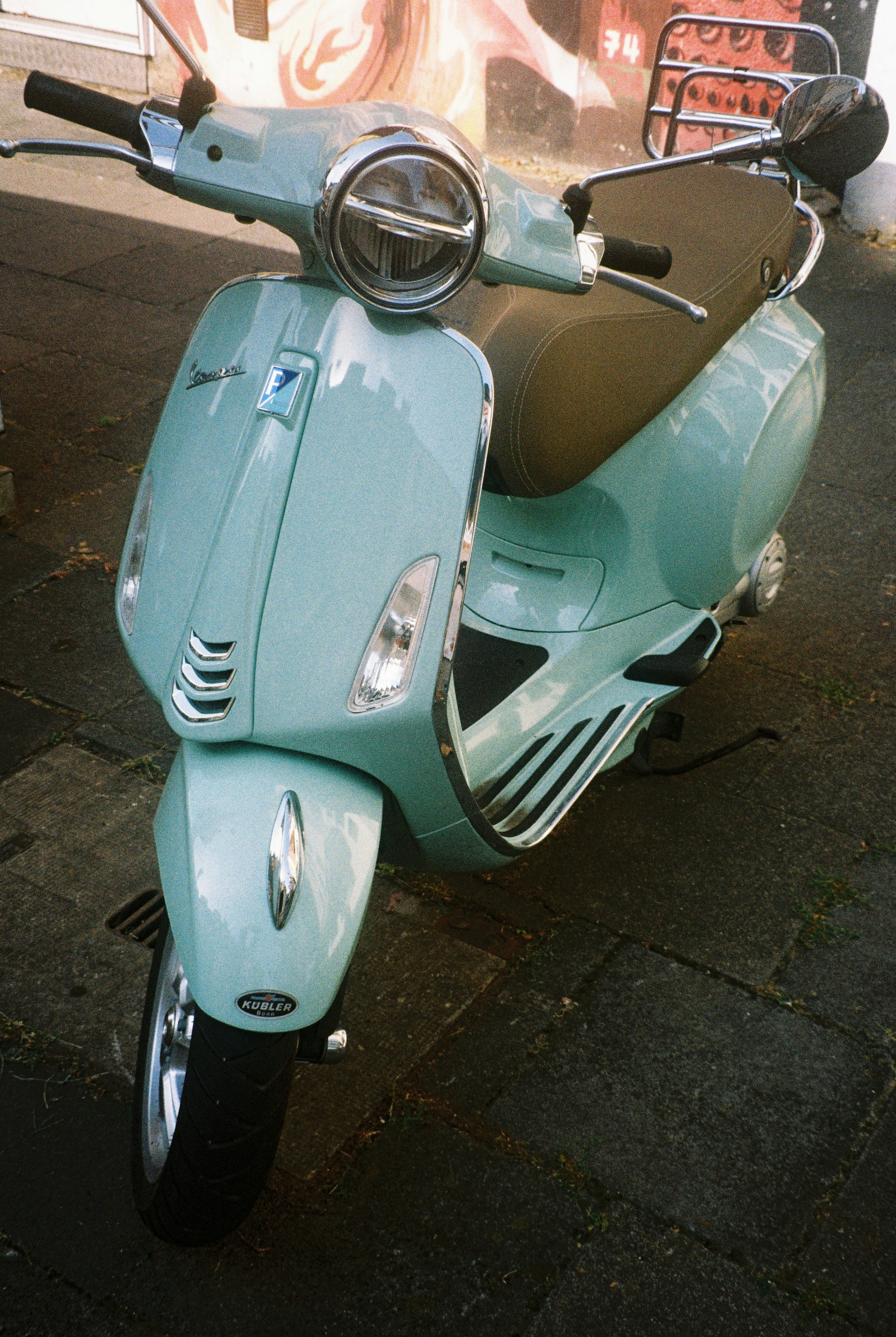 Classic Vespa scooter in a soft aqua color parked on a cobblestone street, showcasing its vintage charm and sleek design.
